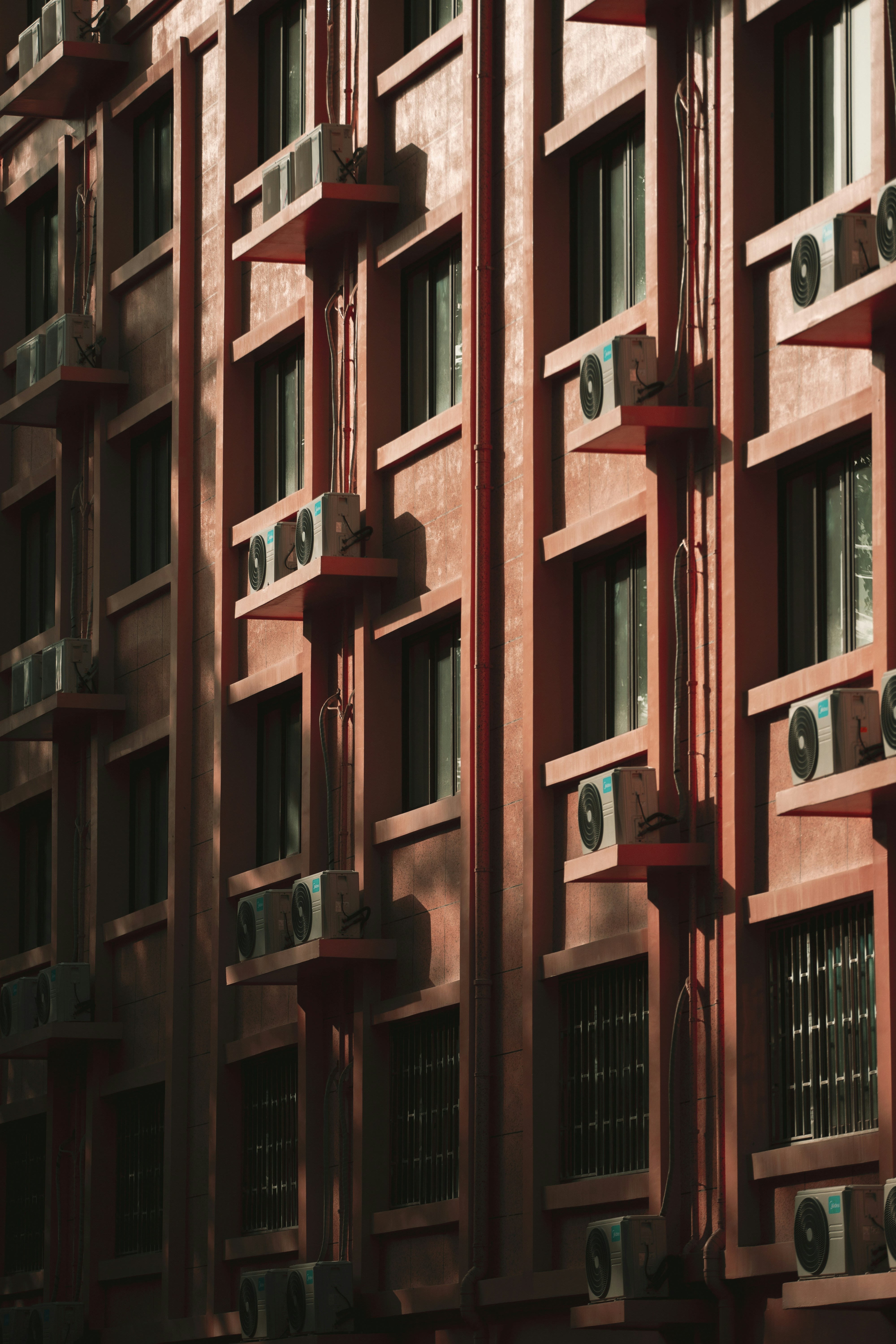 Crimson Facade Grid: Sunlit Air-Conditioners Align on a Red Brick Wall