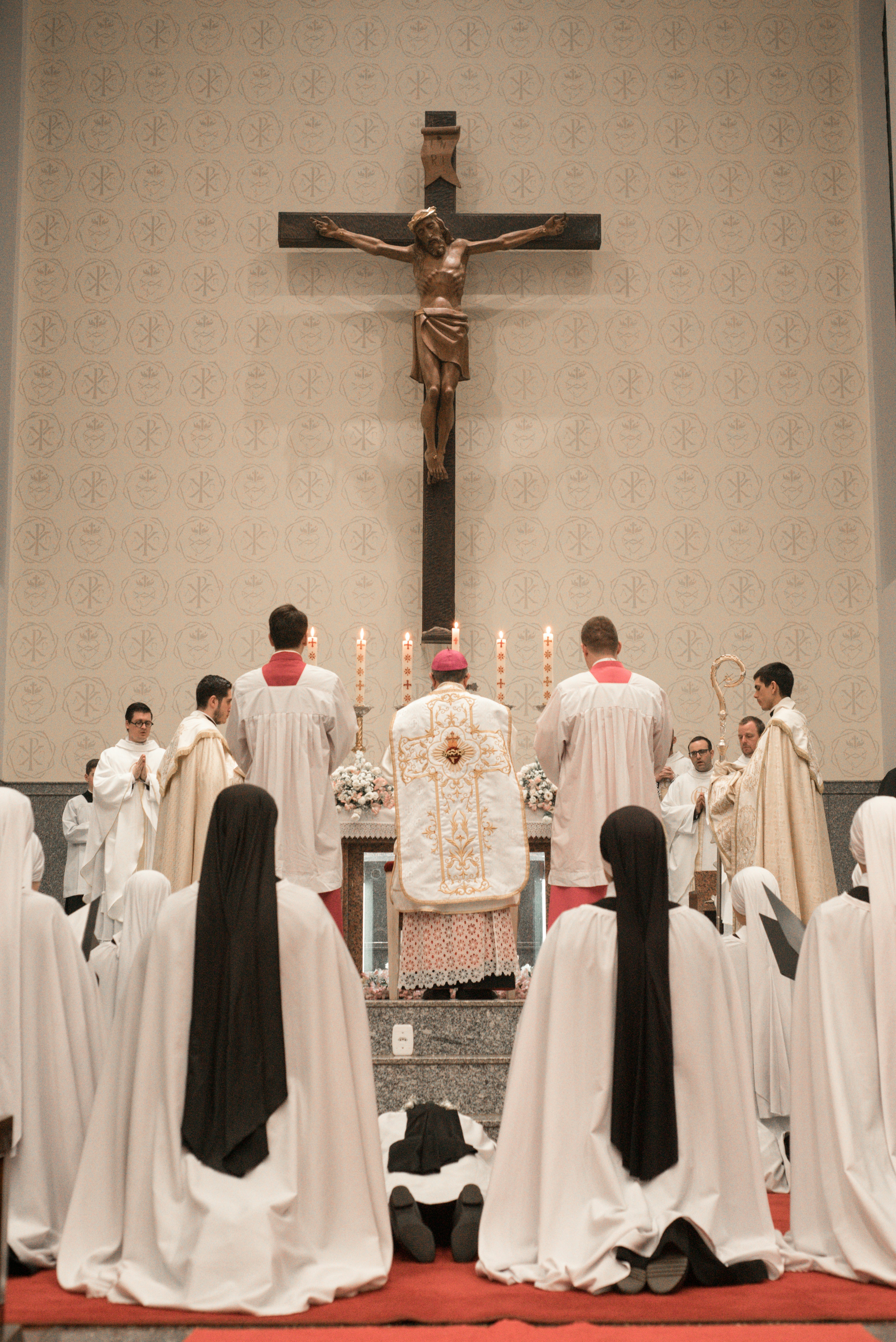 Clergy in white robes kneeling before a large crucifix during a religious ceremony.
