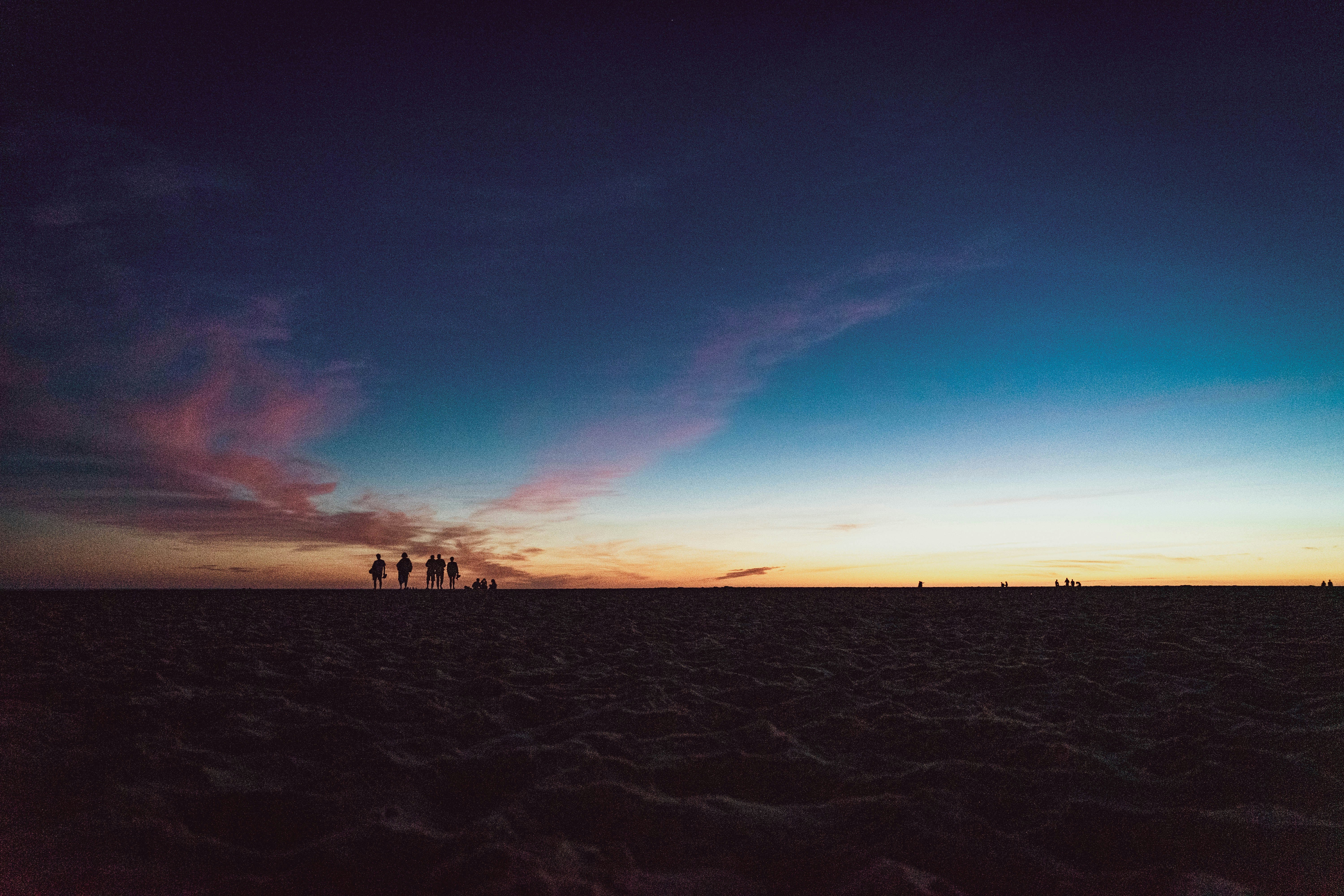 Silhouetted figures walking on a sandy beach against a vibrant sunset sky.