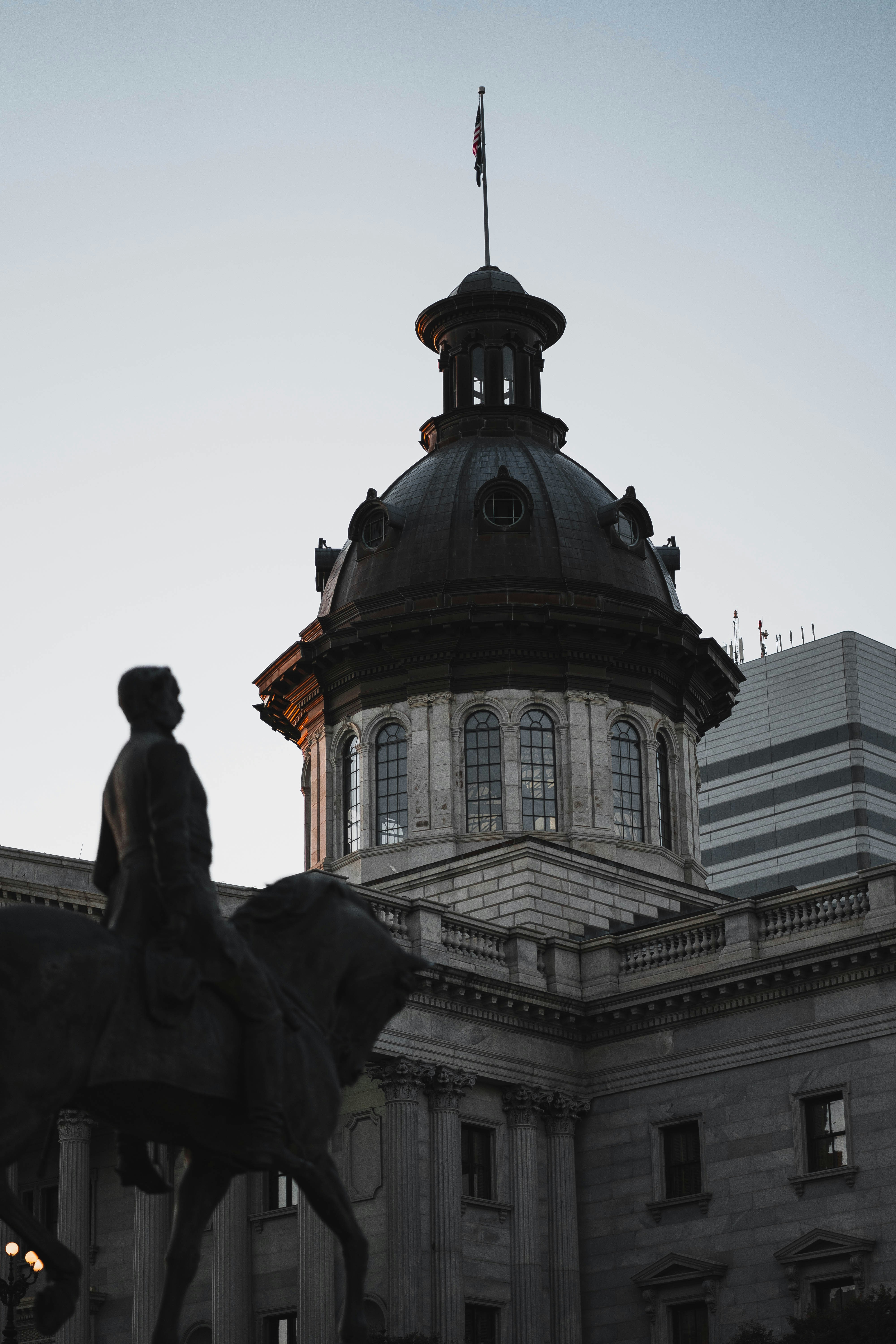 Silhouette of a mounted figure in front of a historic dome, framed by a modern city backdrop.