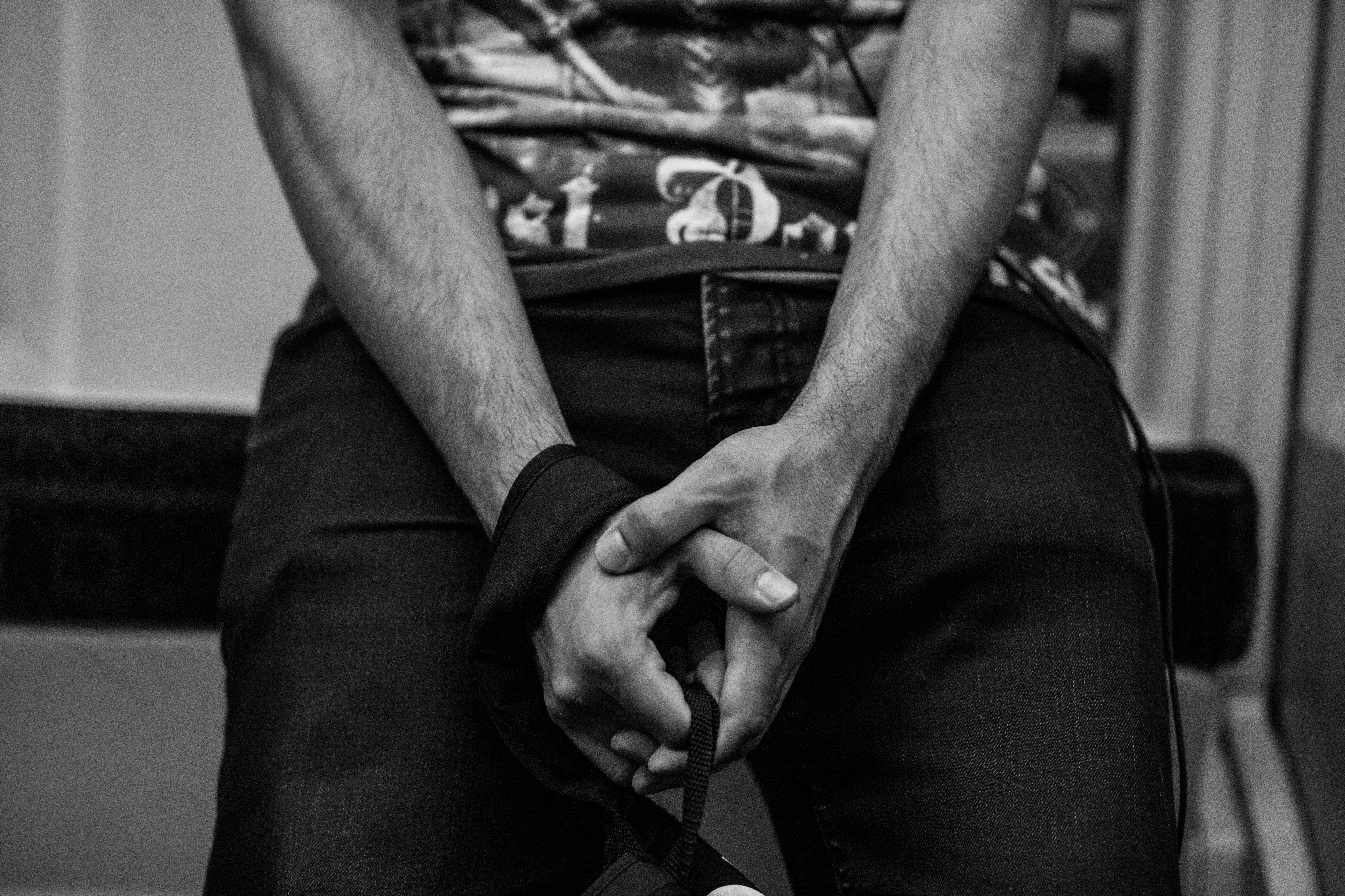Close-up of a person's hands clasped together, conveying a sense of introspection while seated in a public transport setting.