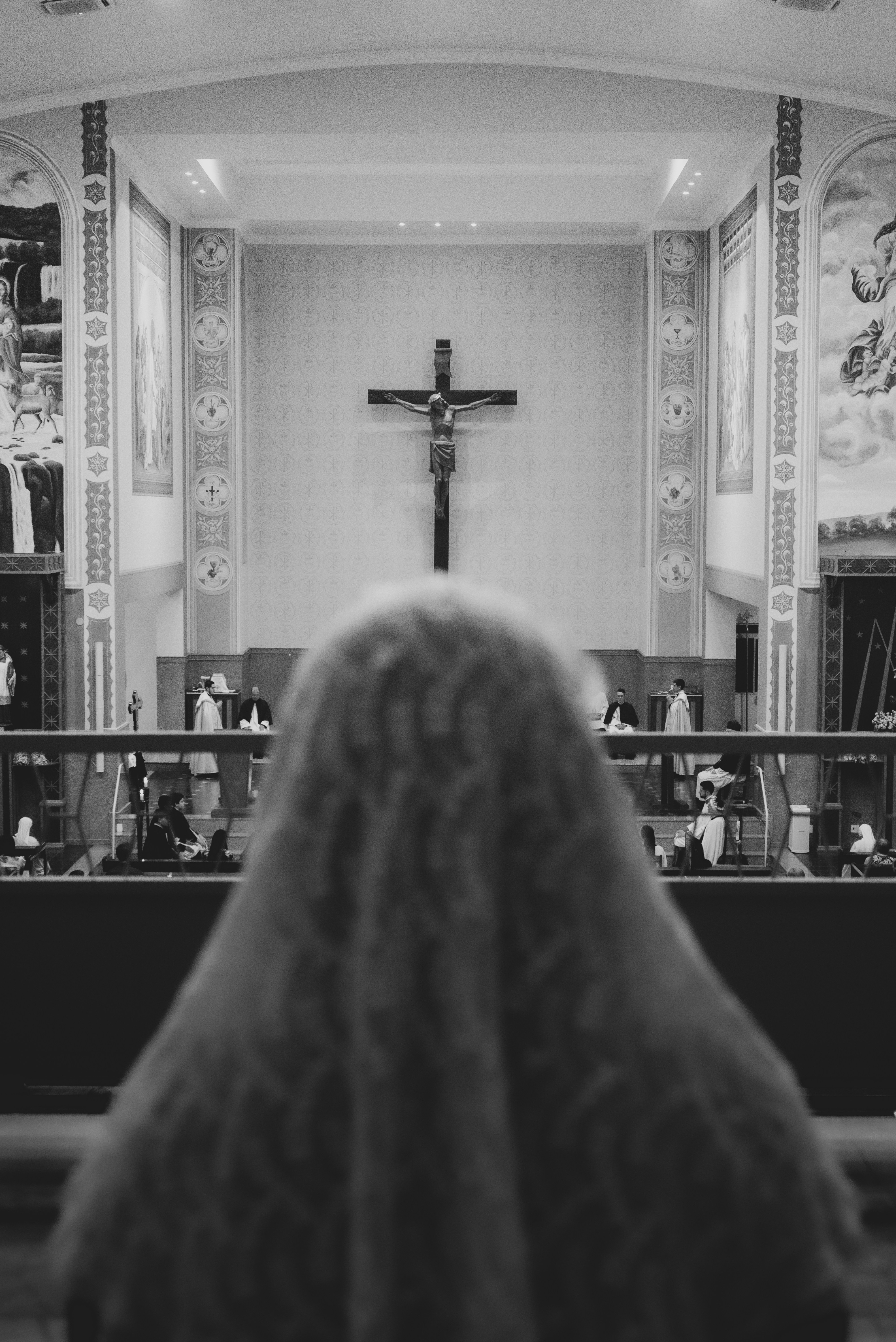 Person in a veil facing a crucifix inside a church, captured in black and white.
