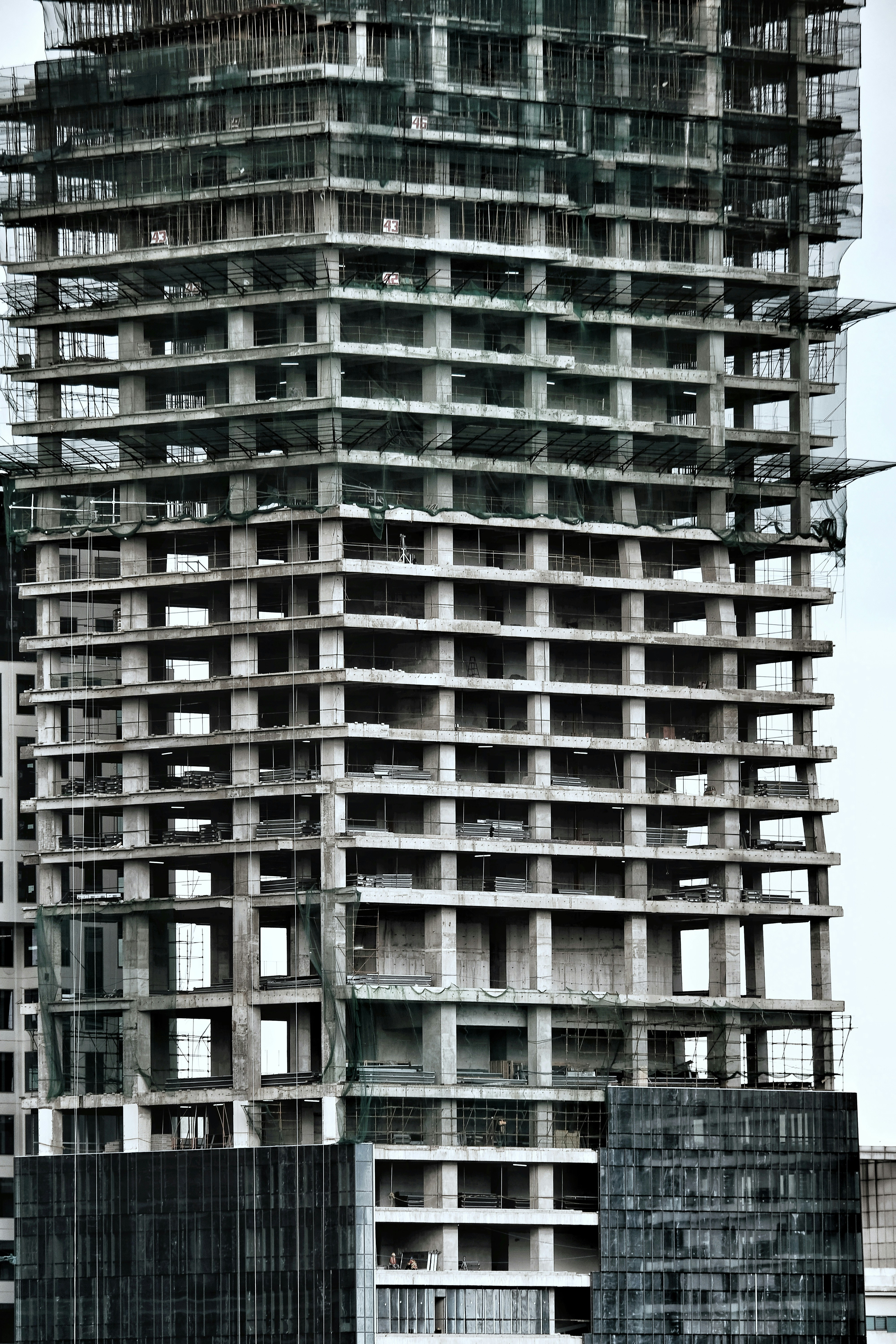 A partially constructed high-rise building showcasing its concrete framework and scaffolding against a cloudy sky.