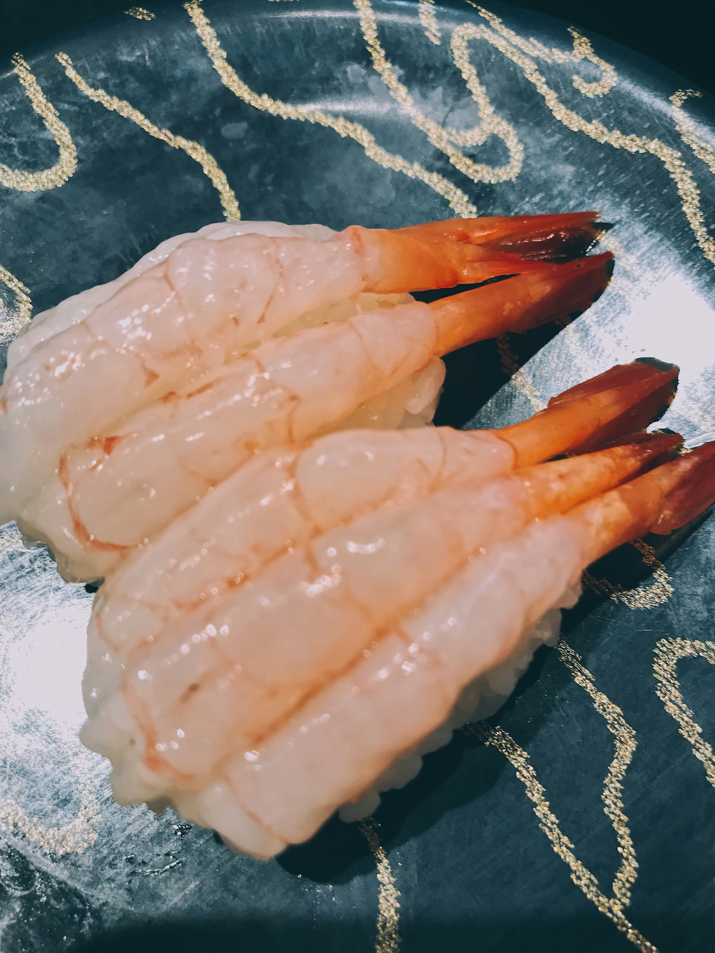 Three pristine shrimp arranged on a decorative black plate with golden swirls.
