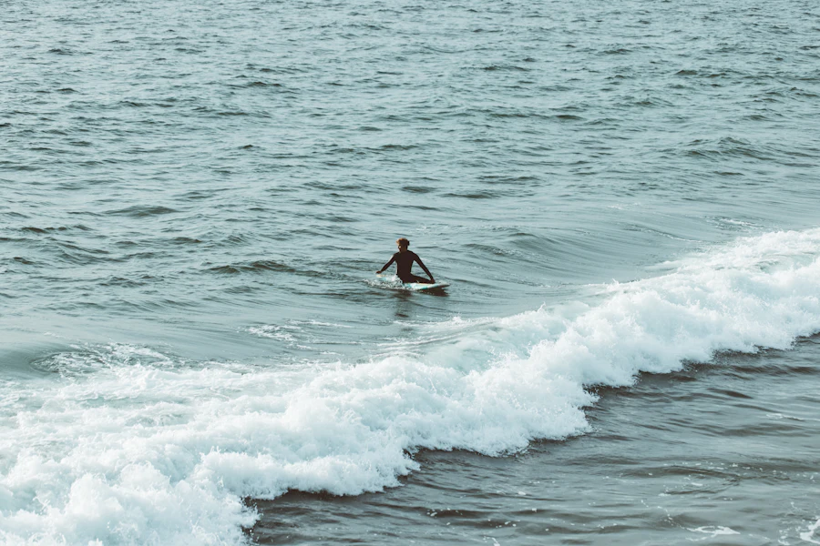 Surfer poised on a board, waiting for the perfect wave amidst the rhythmic dance of the ocean. 