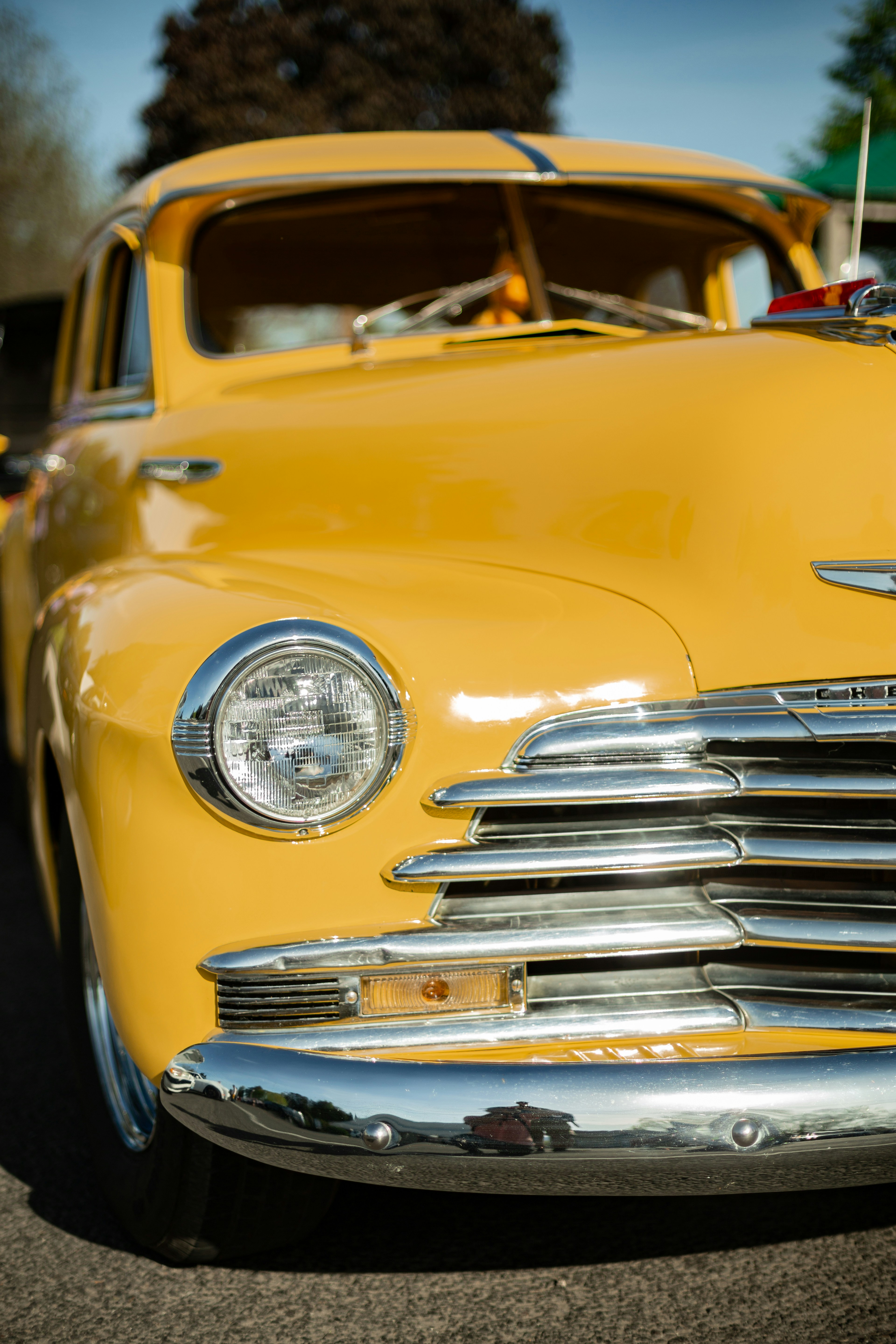 Close-up of a vibrant yellow vintage car showcasing its chrome grille and headlights. The nostalgic design evokes a sense of classic automotive artistry.