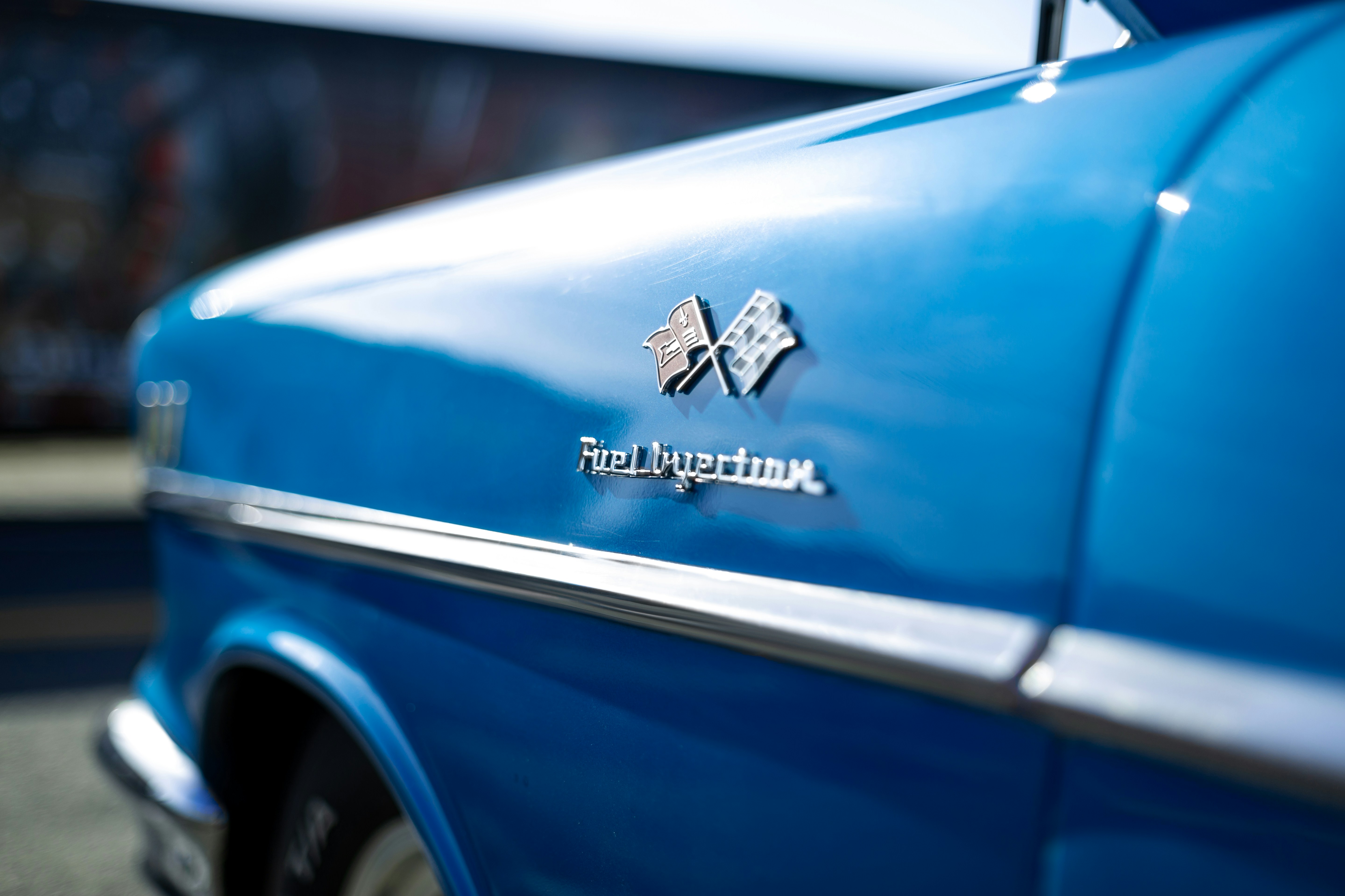 Close-up of a vintage blue car's emblem and paintwork, highlighting its classic design and craftsmanship.