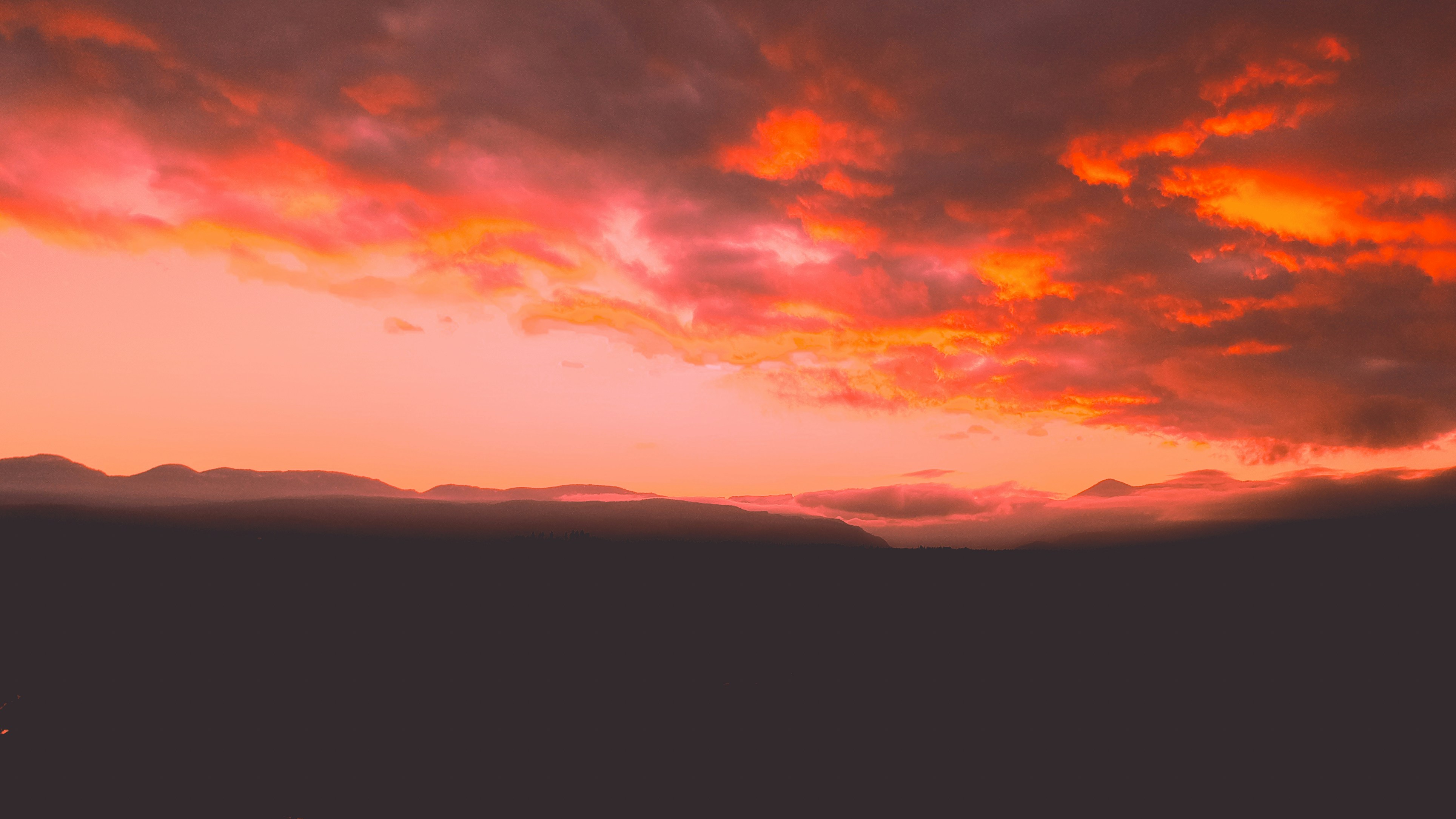 Vibrant orange and pink clouds dominate the sky above a silhouetted mountain range at sunset.