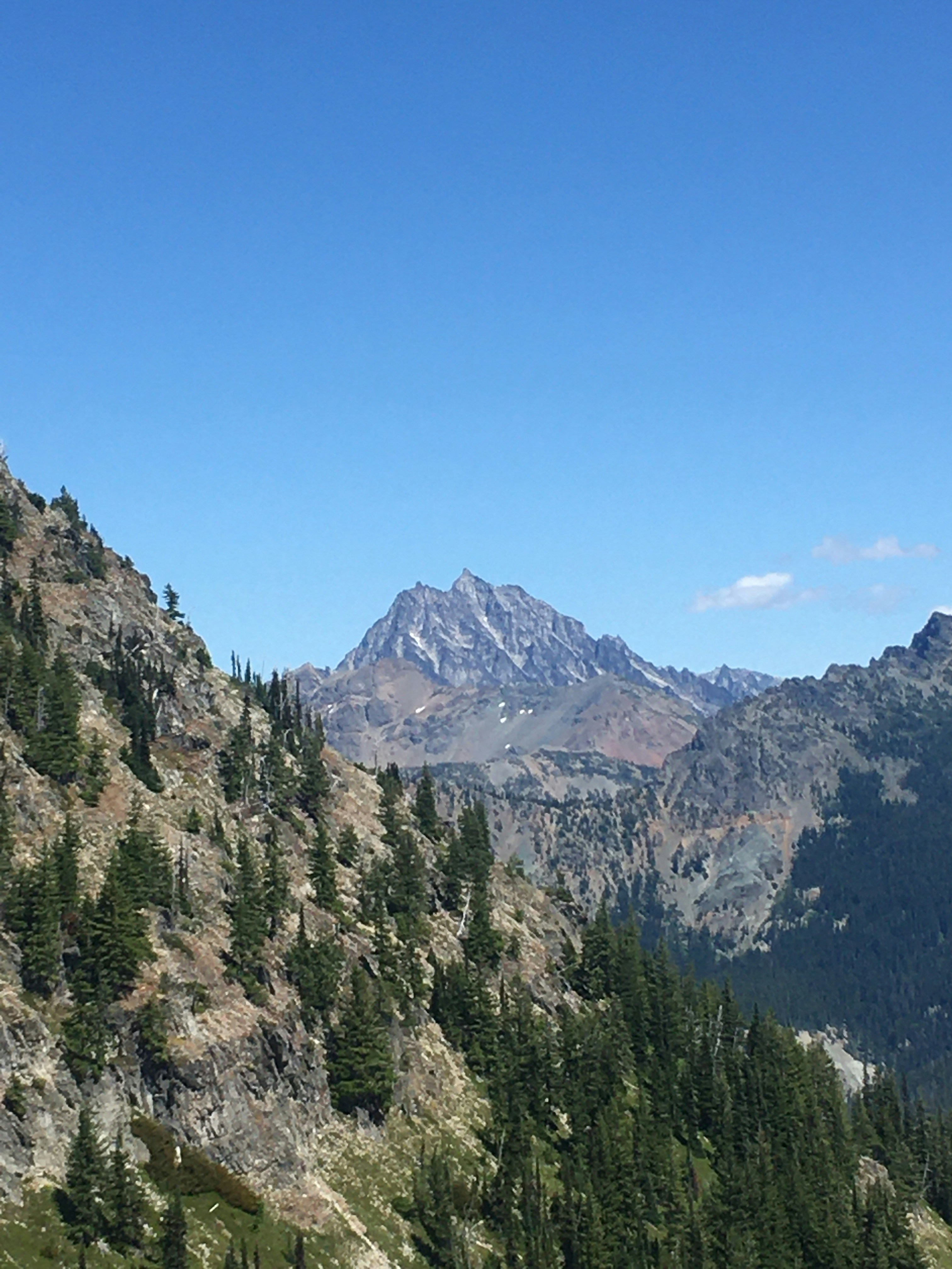 Majestic mountain range with lush greenery in the foreground, showcasing rugged peaks under a clear blue sky.