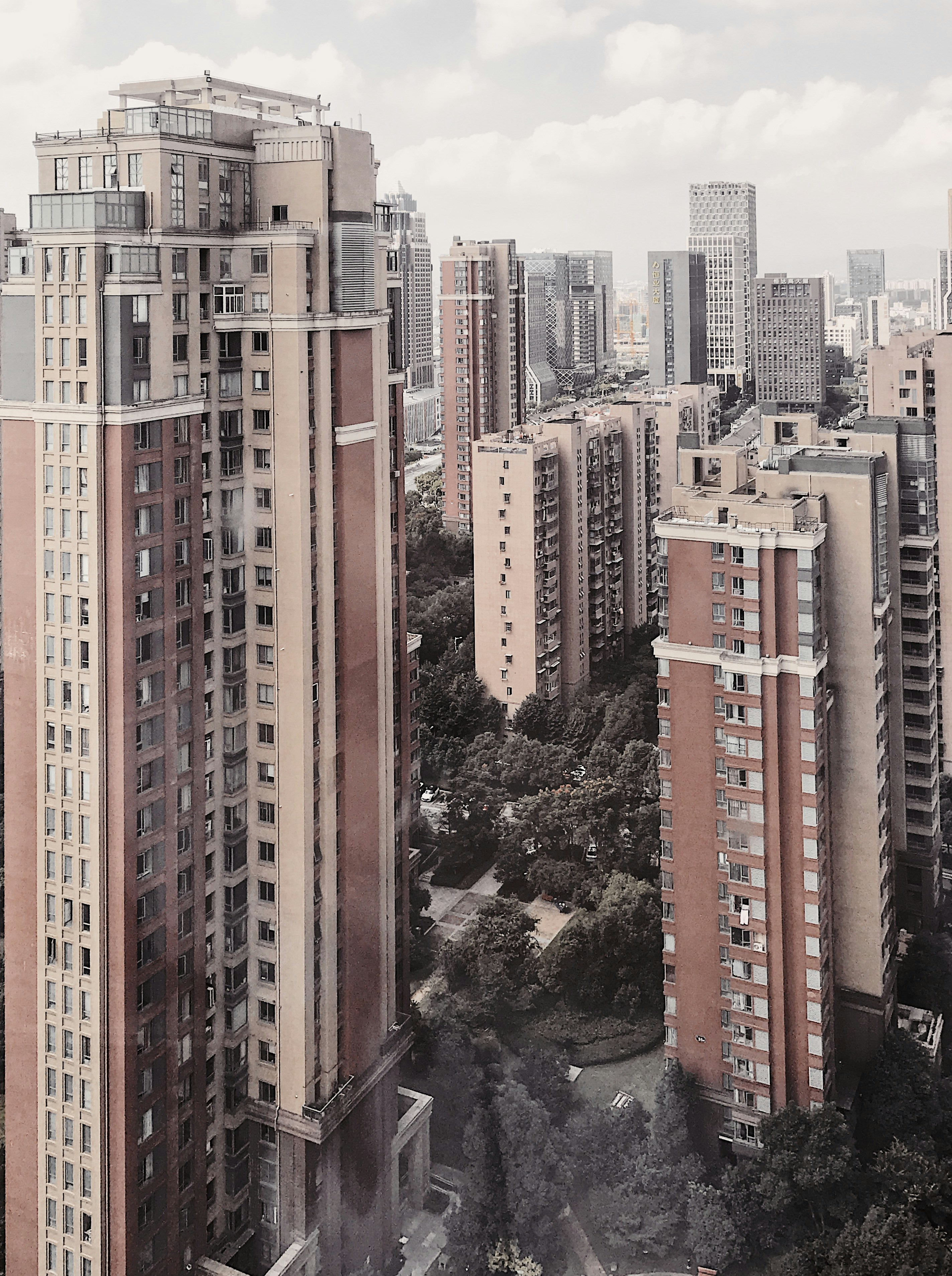 Aerial view of a dense urban landscape showcasing high-rise buildings and lush greenery below. The juxtaposition of concrete and nature creates a striking visual narrative.