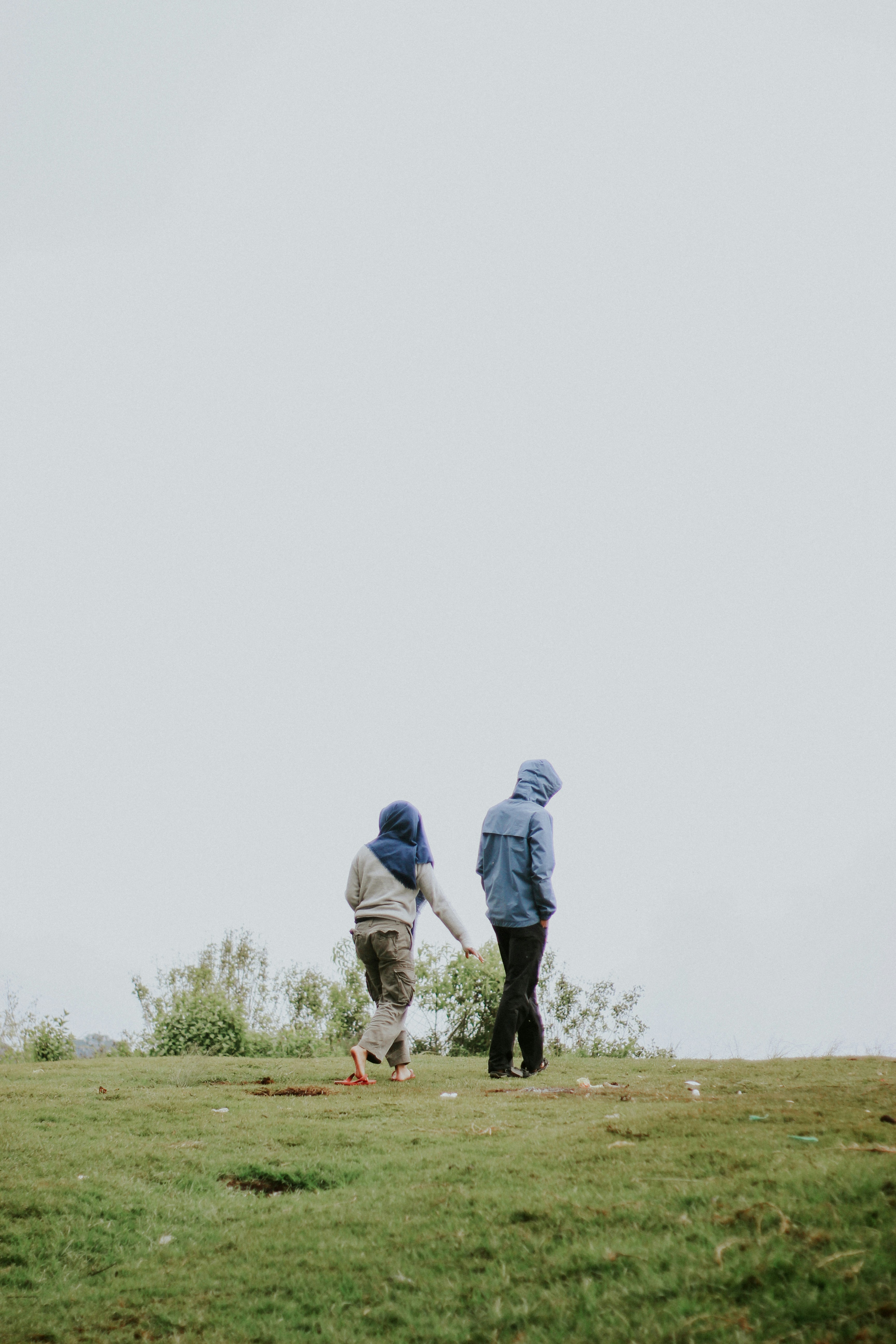Two Hooded Figures Walk Hand in Hand Across a Quiet Hill