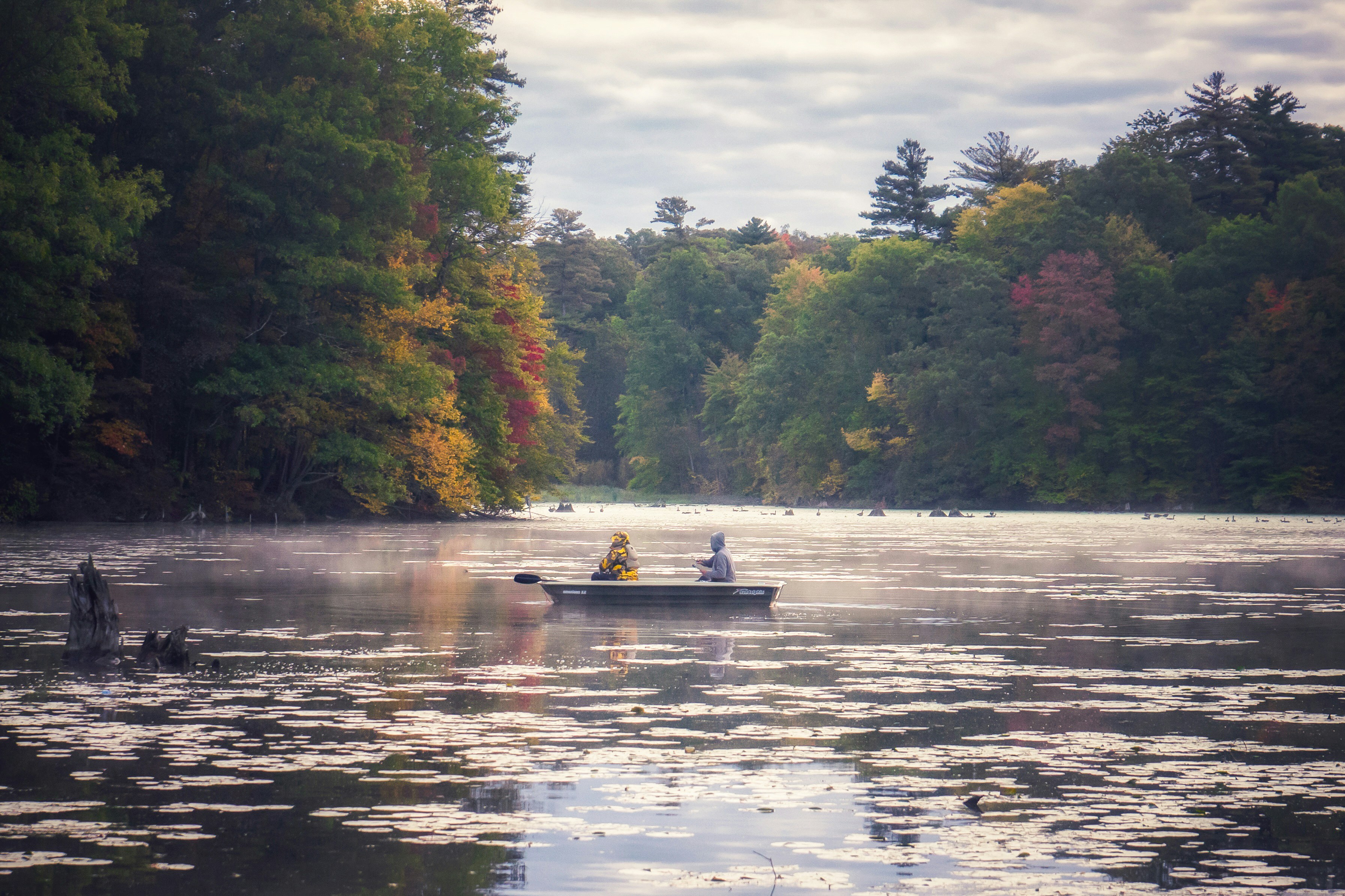 Two men fish in a boat in the fall colours.