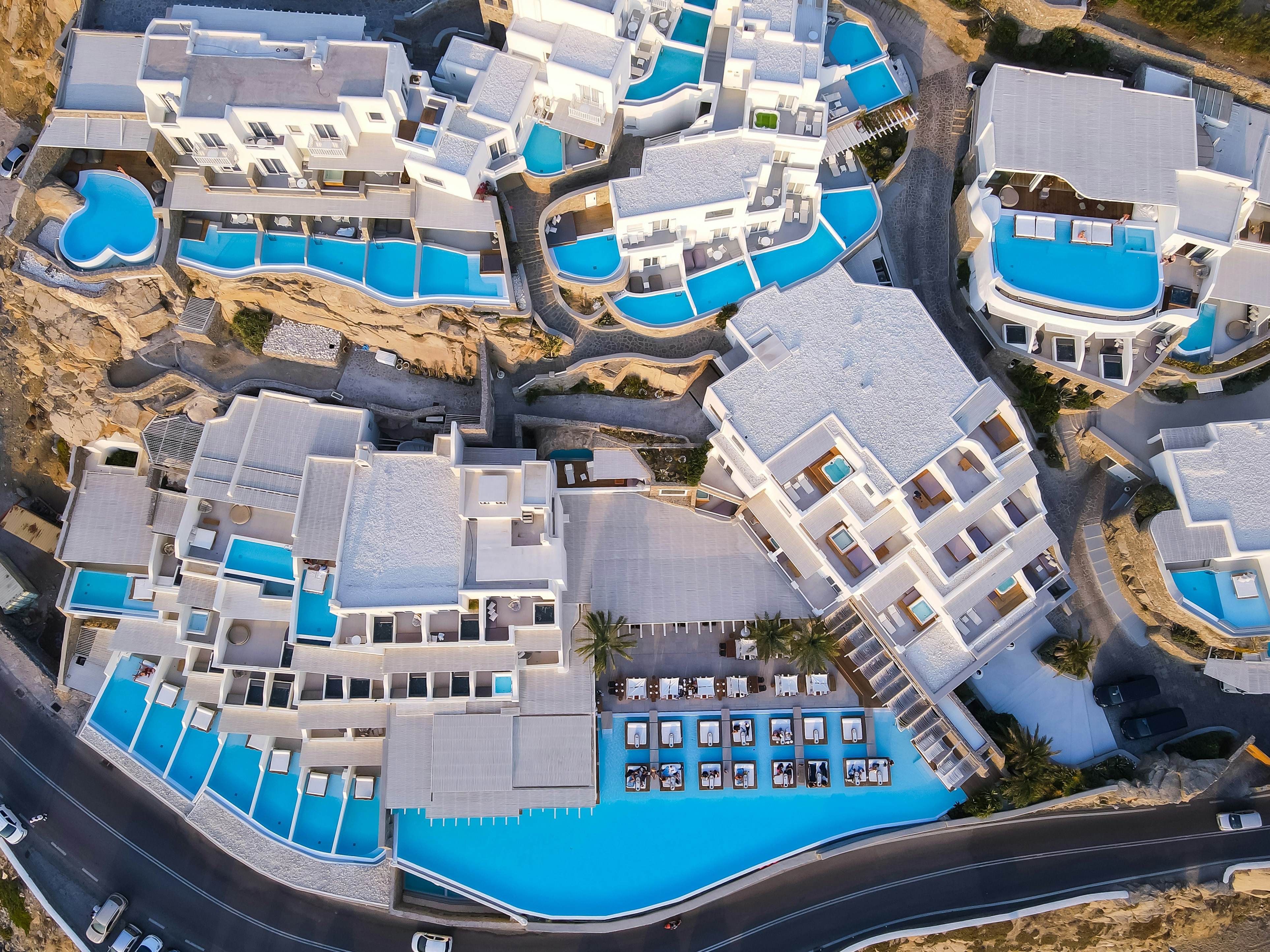 Luxurious white buildings with blue pools arranged in a geometric pattern viewed from above.