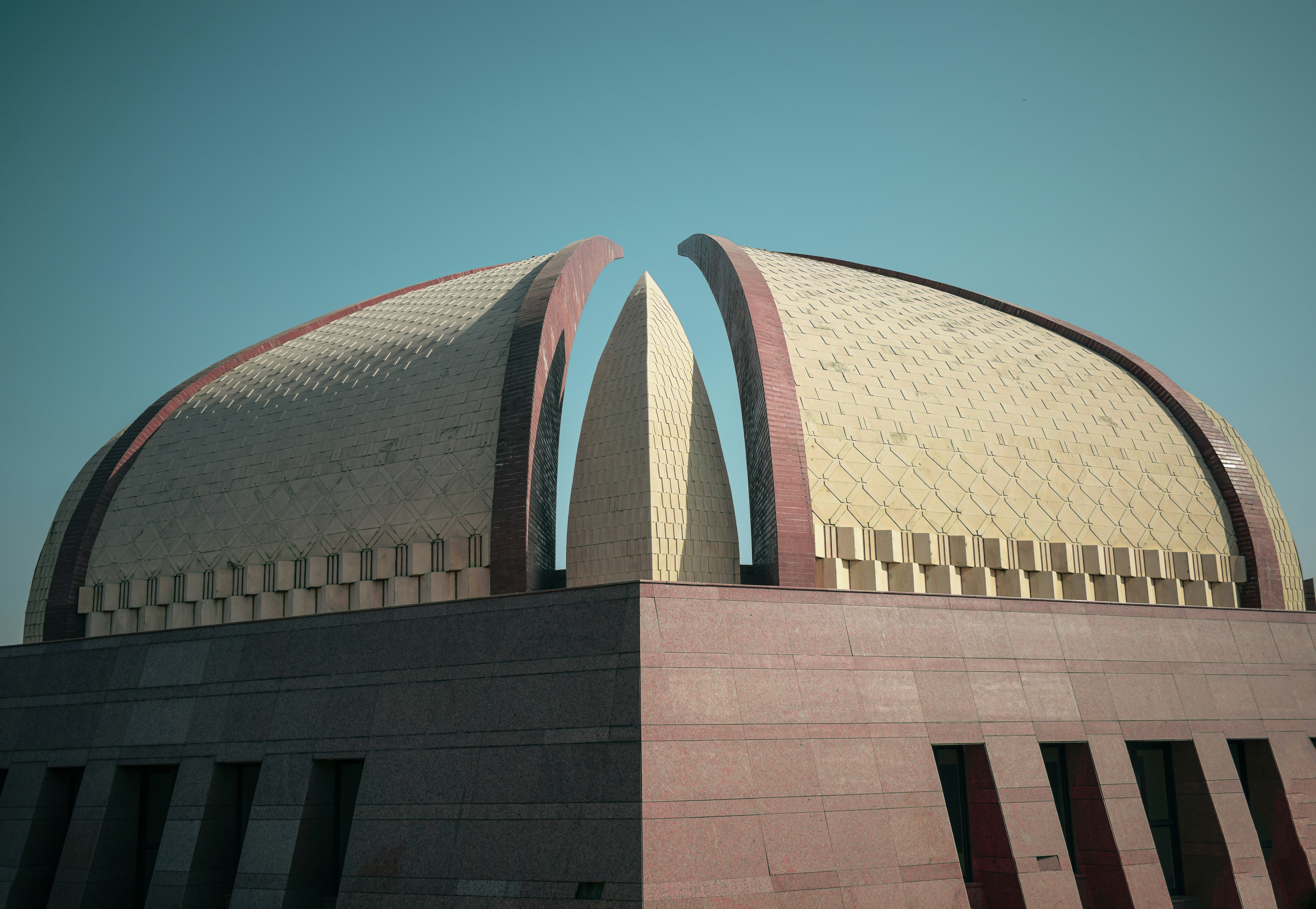 A modern architectural structure featuring two curved roofs that elegantly meet at a central point, showcasing intricate design details and a blend of materials.