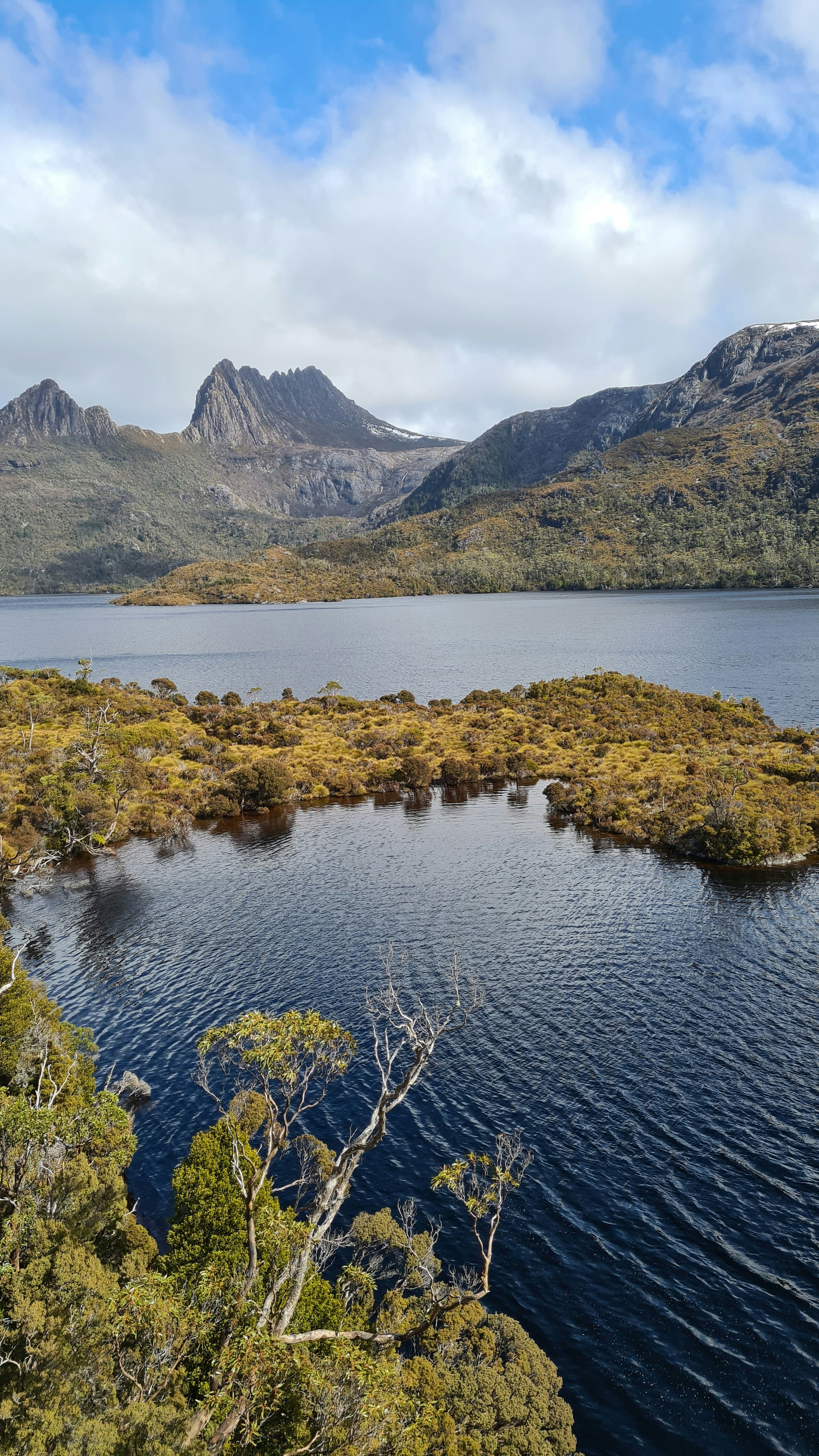 Lush greenery meets tranquil waters, framed by towering mountains under a partly cloudy sky. The scene captures the essence of untouched nature.