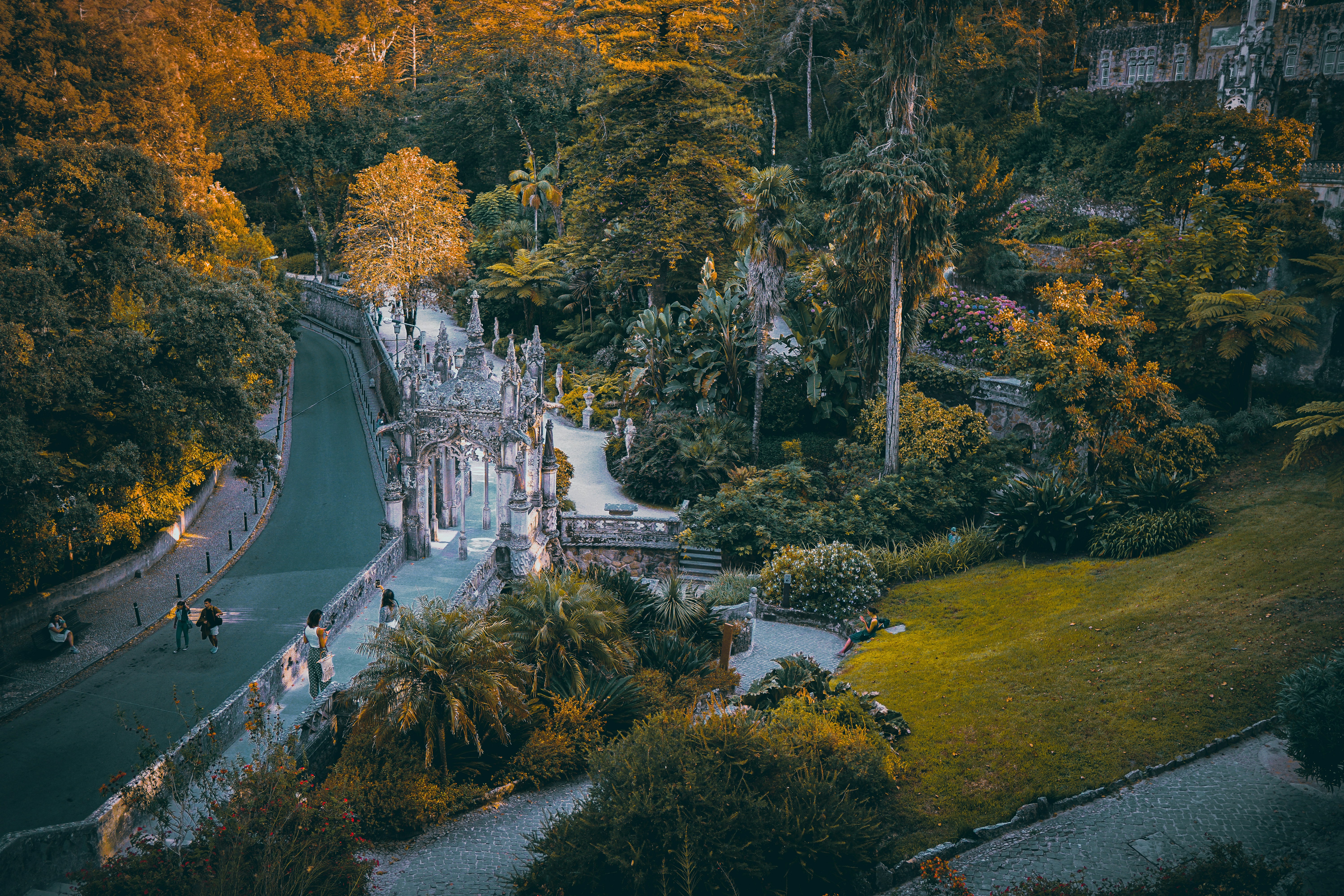 Ornate stone archway amidst vibrant green and golden-hued trees in a tranquil garden setting.