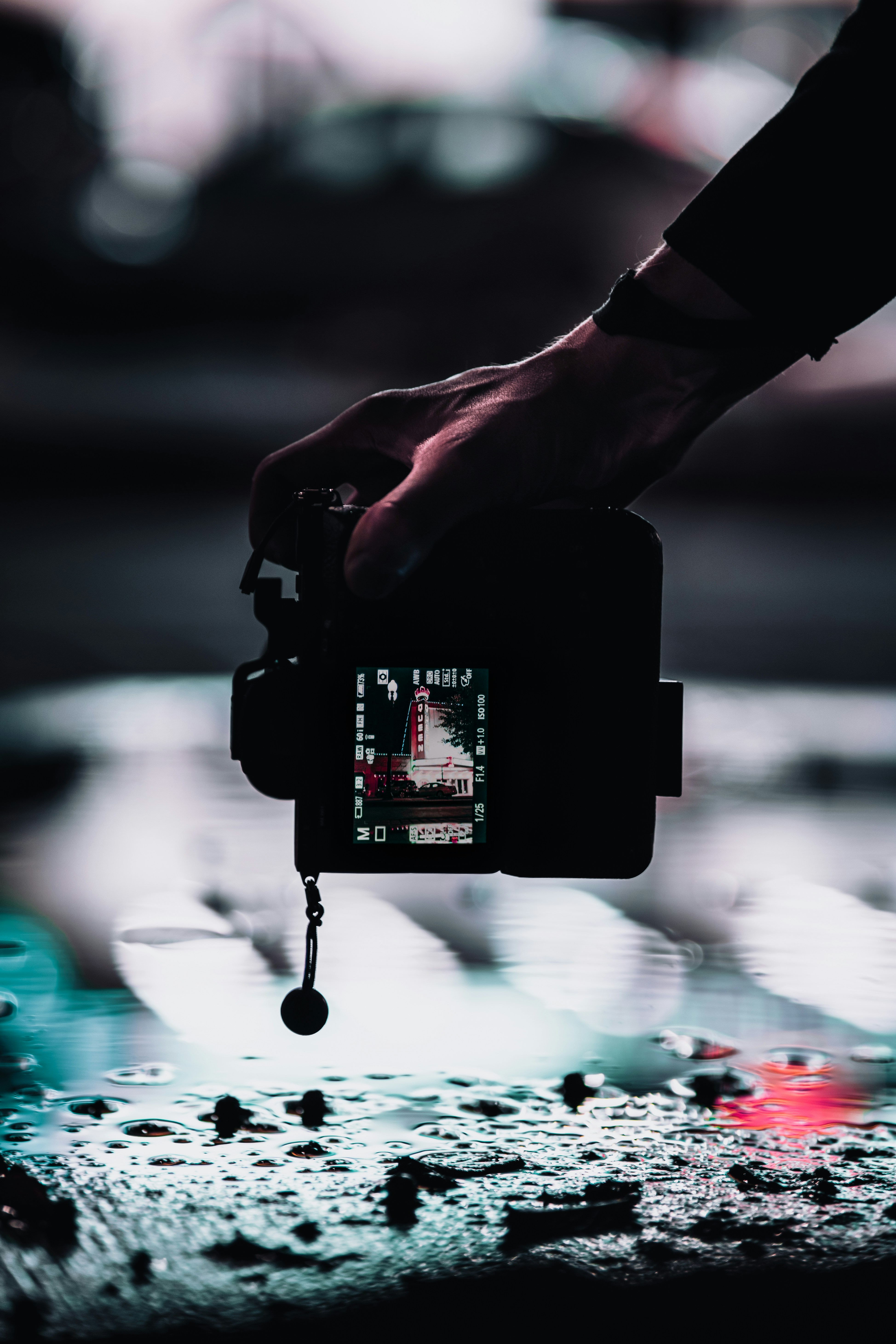 Moody Night Grip: A Silhouette Clutches a Camera Over a Rain-Slicked, Neon-Reflected Street