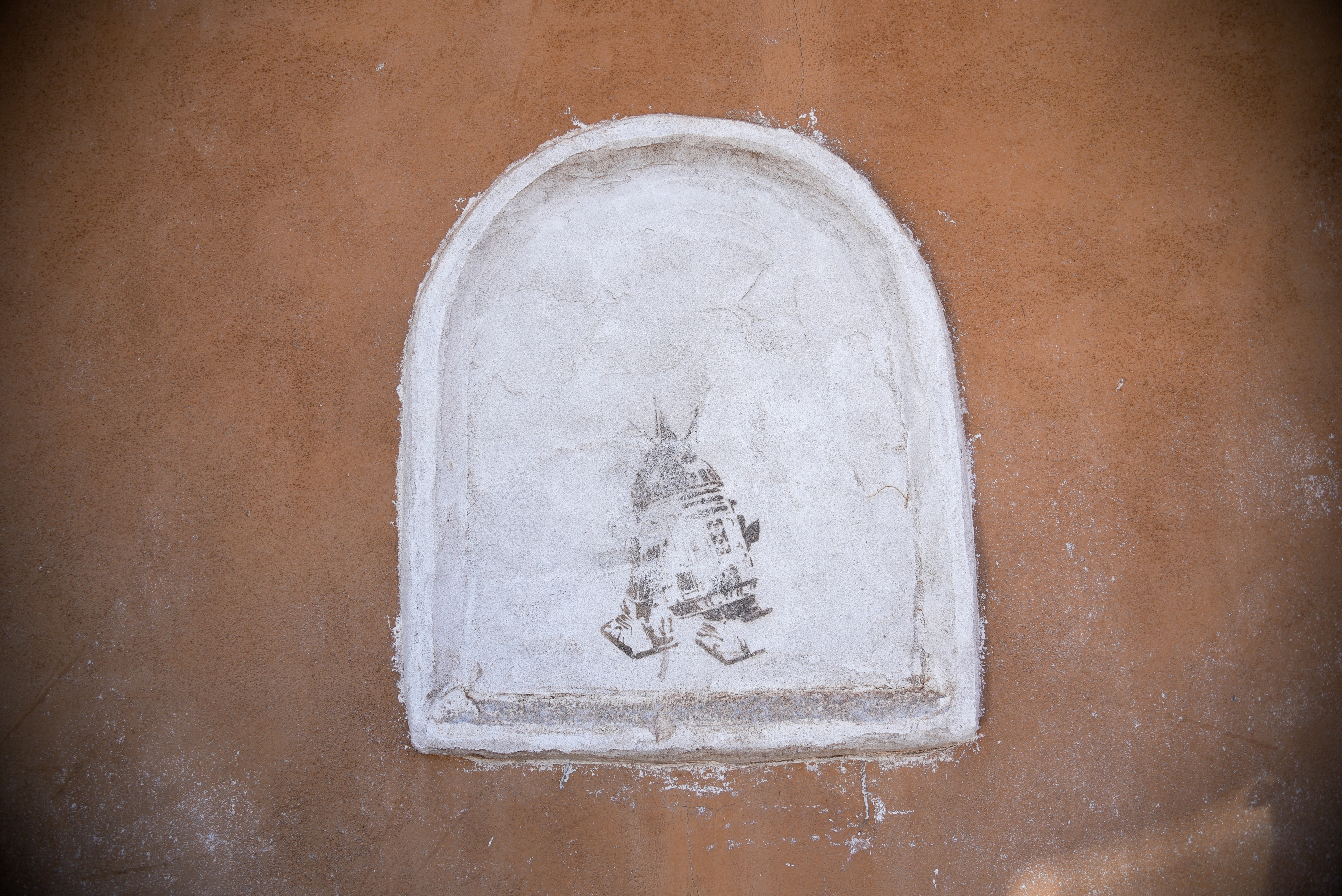 Small arched niche with a faded illustration on a textured, earthen wall.