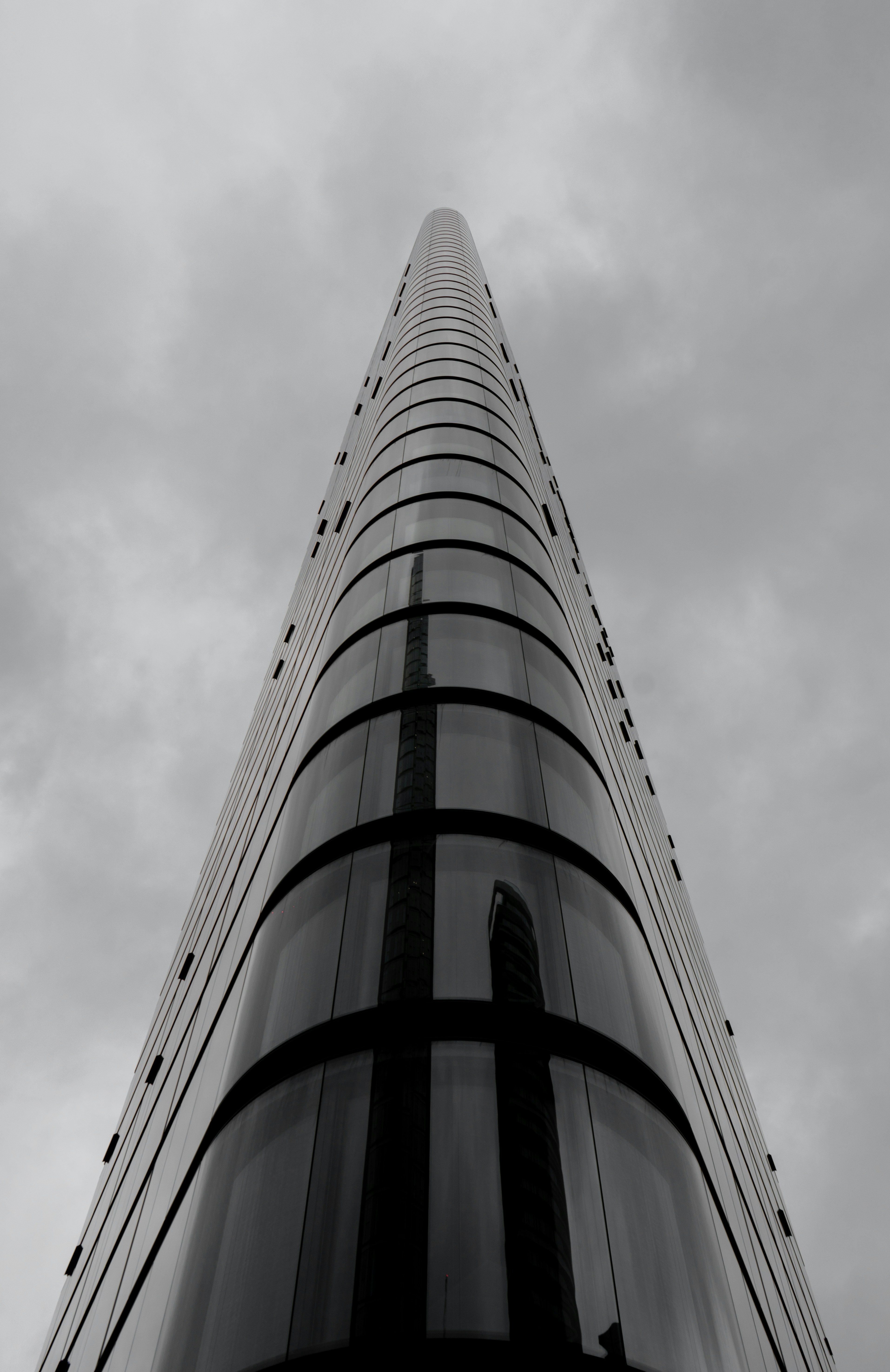 Sleek modern skyscraper viewed from below, showcasing its reflective glass facade against a cloudy sky.