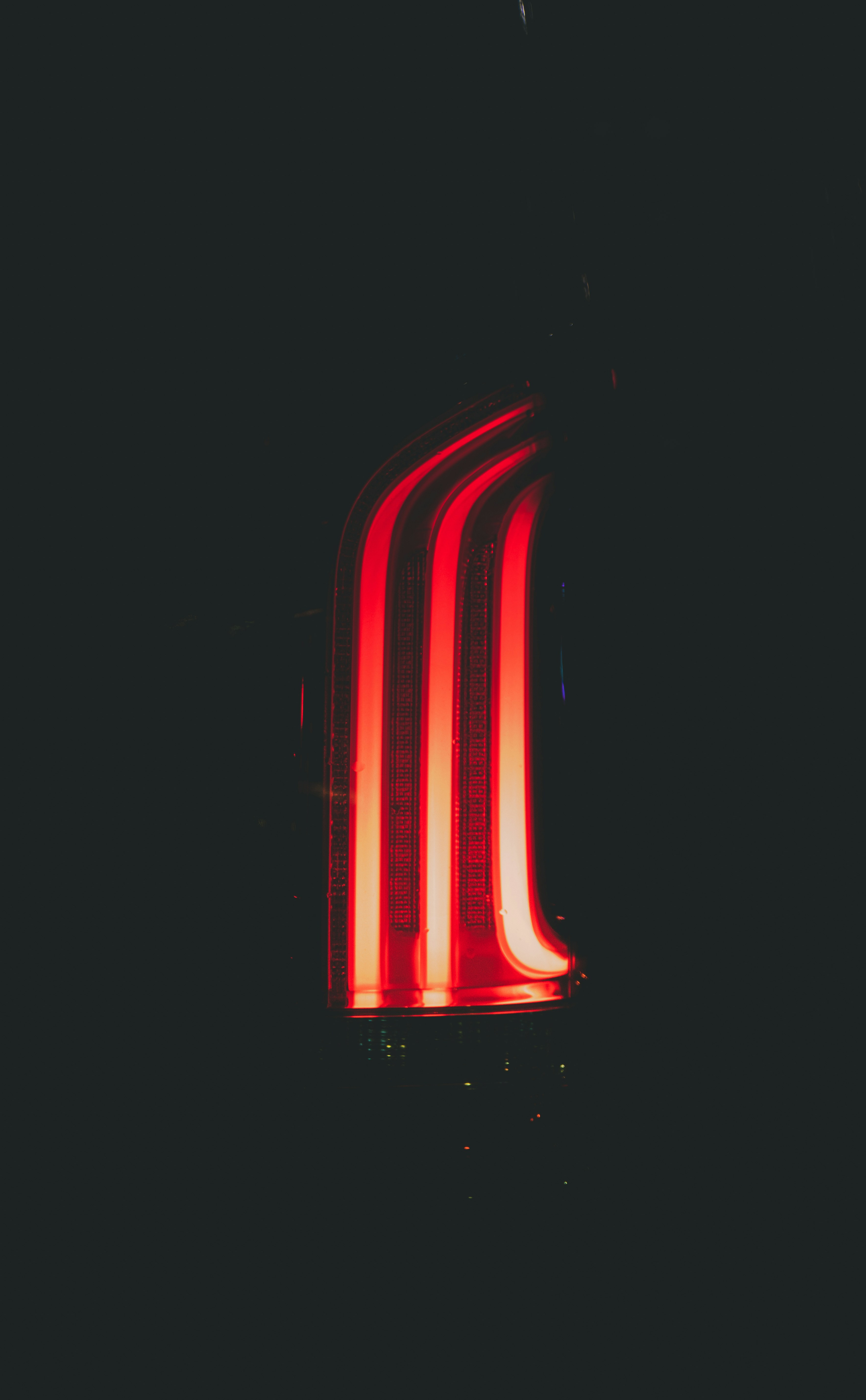 Close-up of an illuminated red taillight with sleek vertical lines against a dark background.