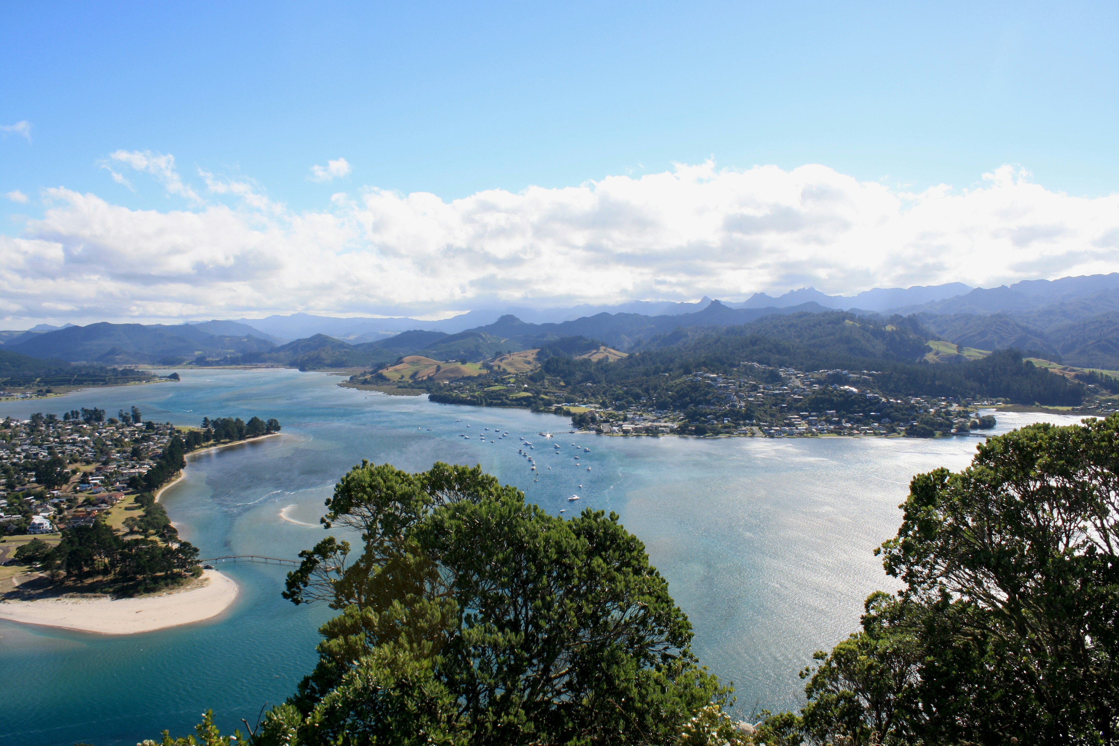 Expansive view of a bay with winding shoreline and distant mountains under a bright blue sky.