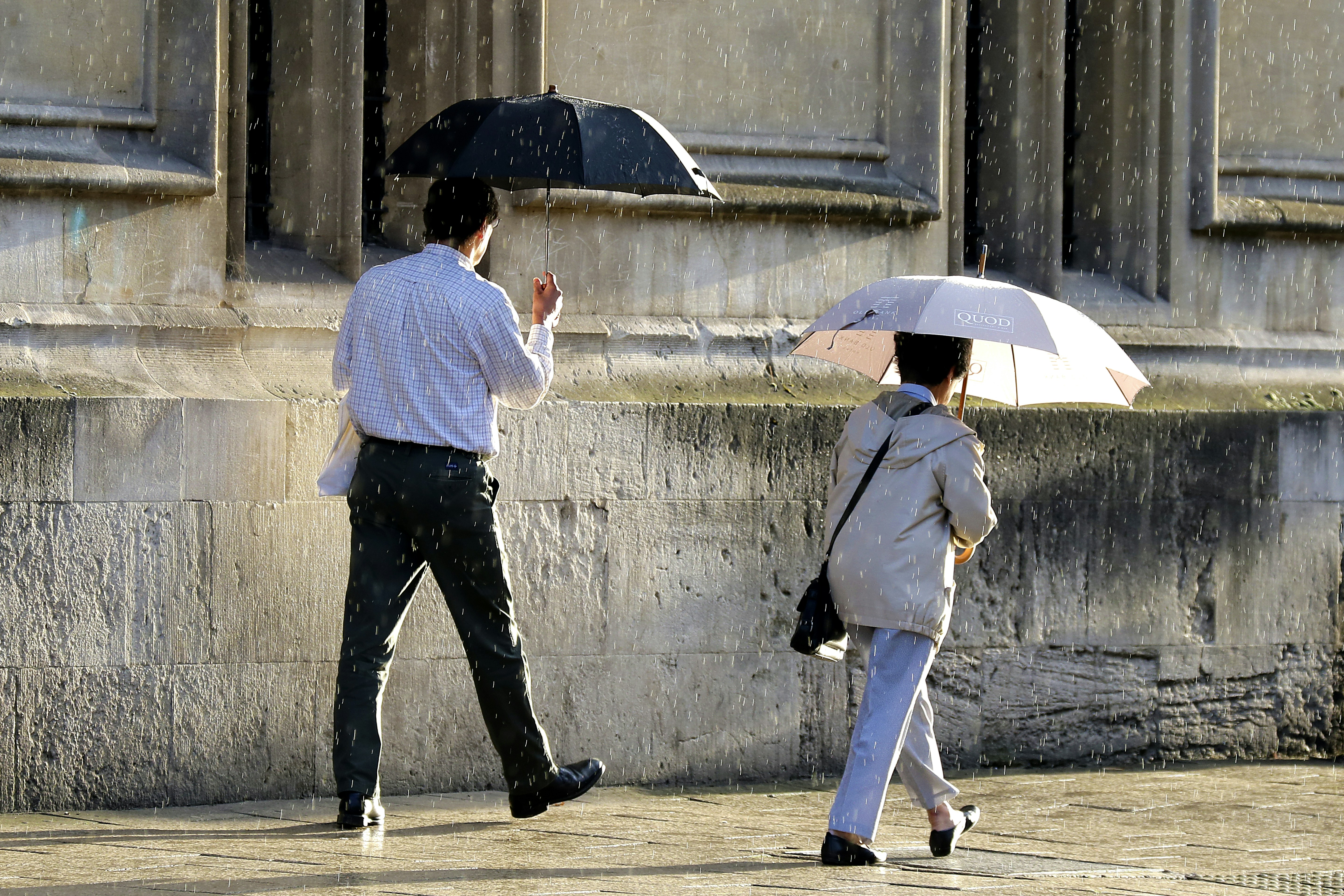 man in white shirt and black pants holding umbrella while walking on sidewalk during daytime