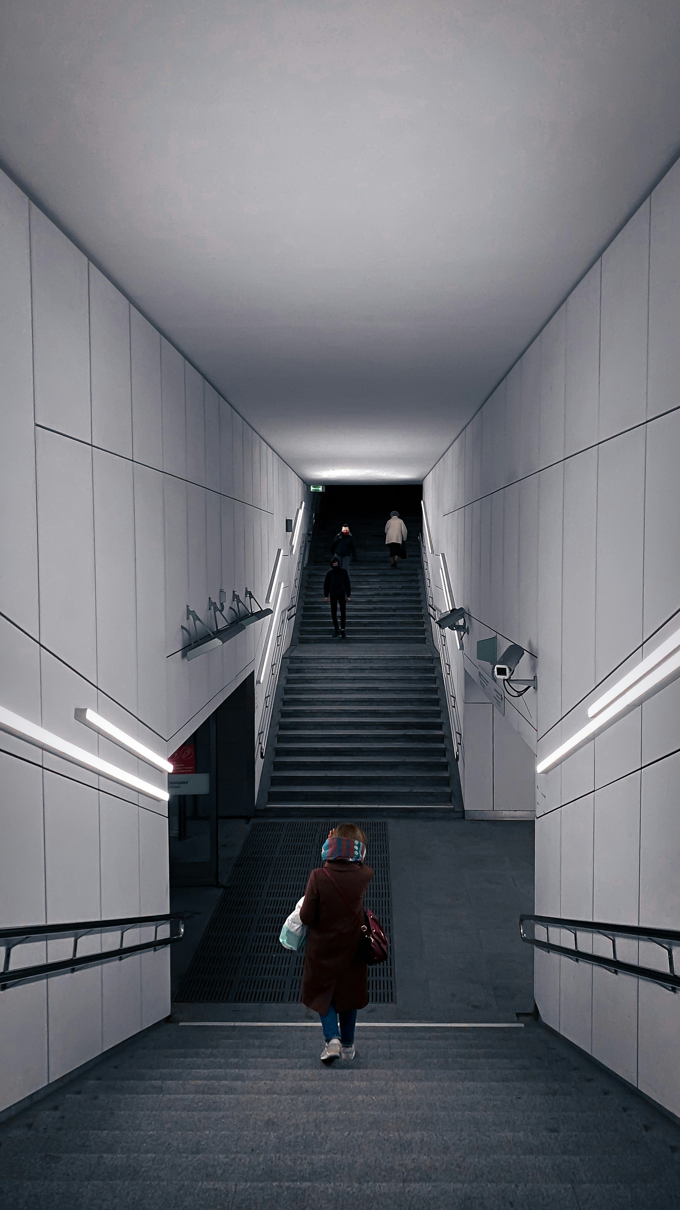Stairwell to Light: A solitary traveler ascends through a stark transit tunnel