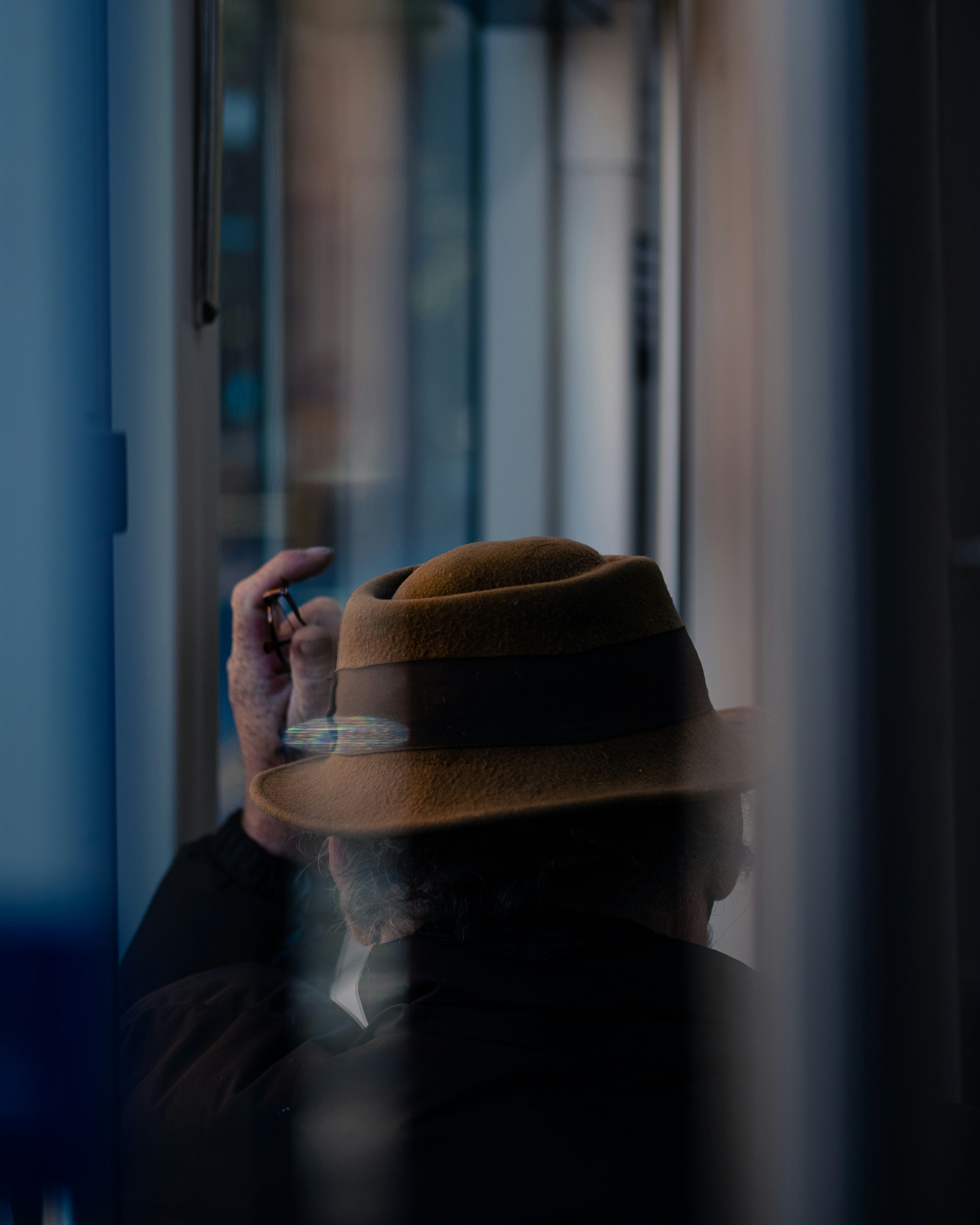 An elderly figure with a hat, seen through a translucent barrier, exudes a sense of contemplation and solitude.