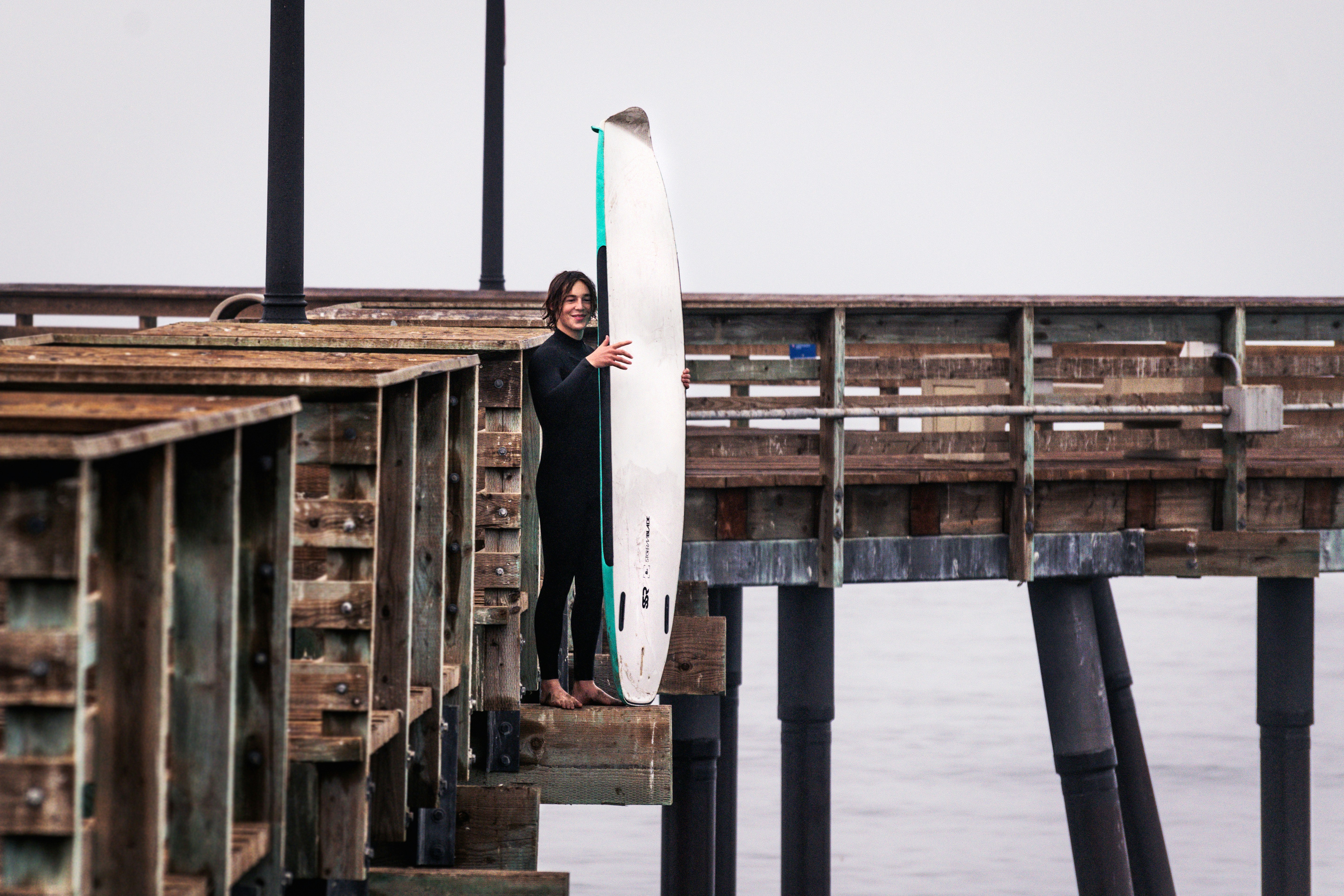 Surfer on a Weathered Pier, Ready to Ride the Quiet Horizon