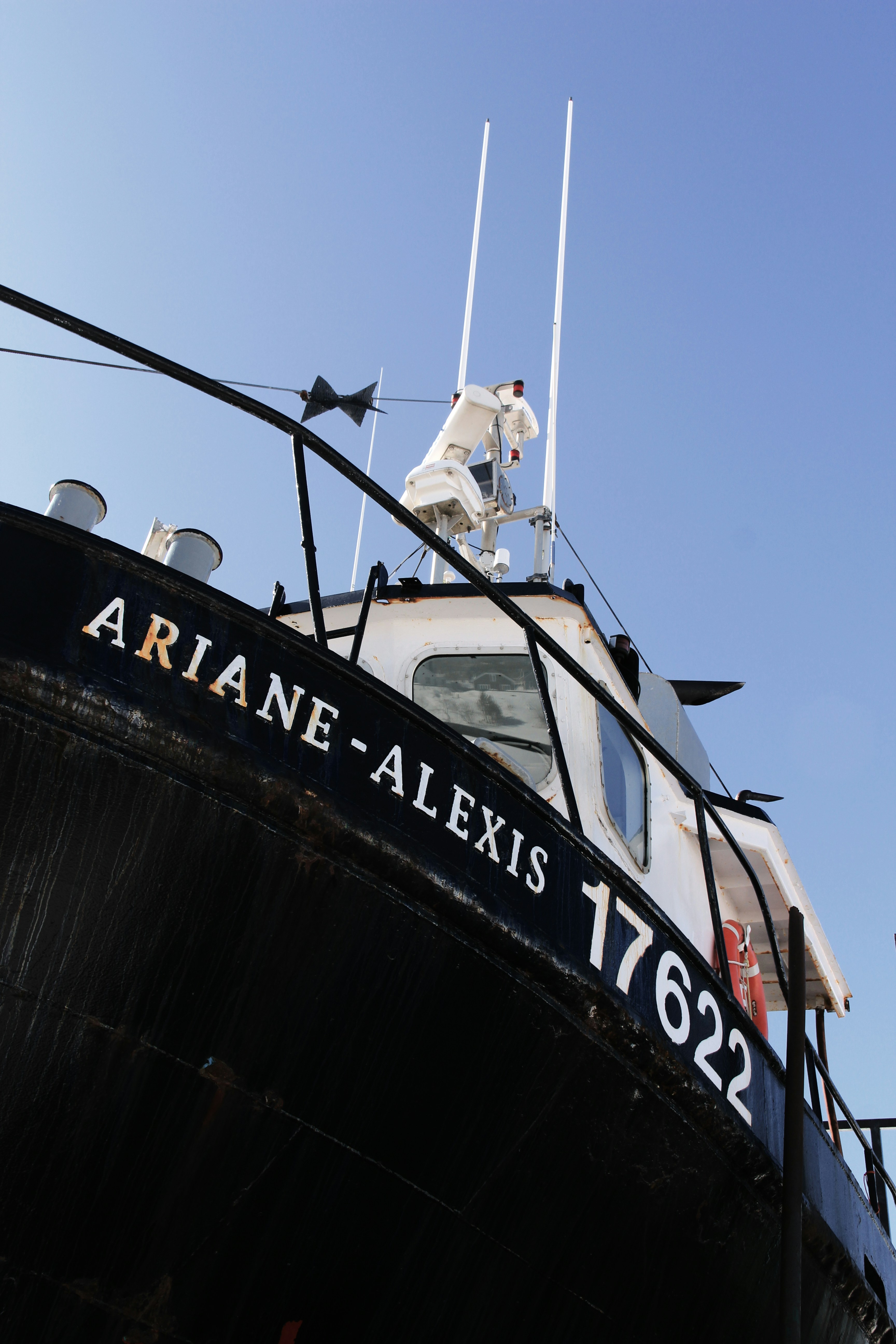 The bow of the Ariane-Alexis fishing vessel rises against a clear blue sky, showcasing its name and registration number prominently.