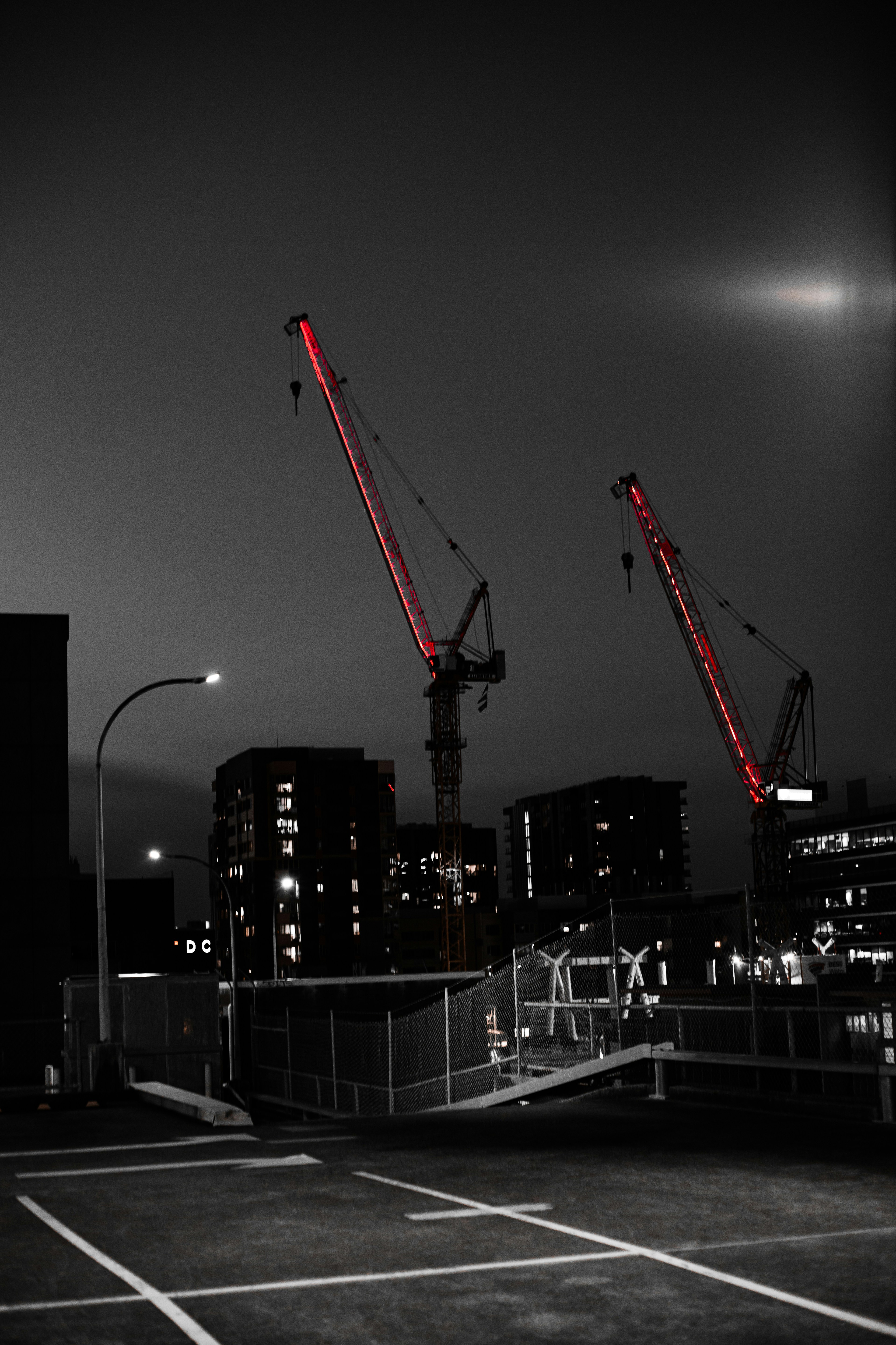 Red-lit cranes over a monochrome cityscape at night