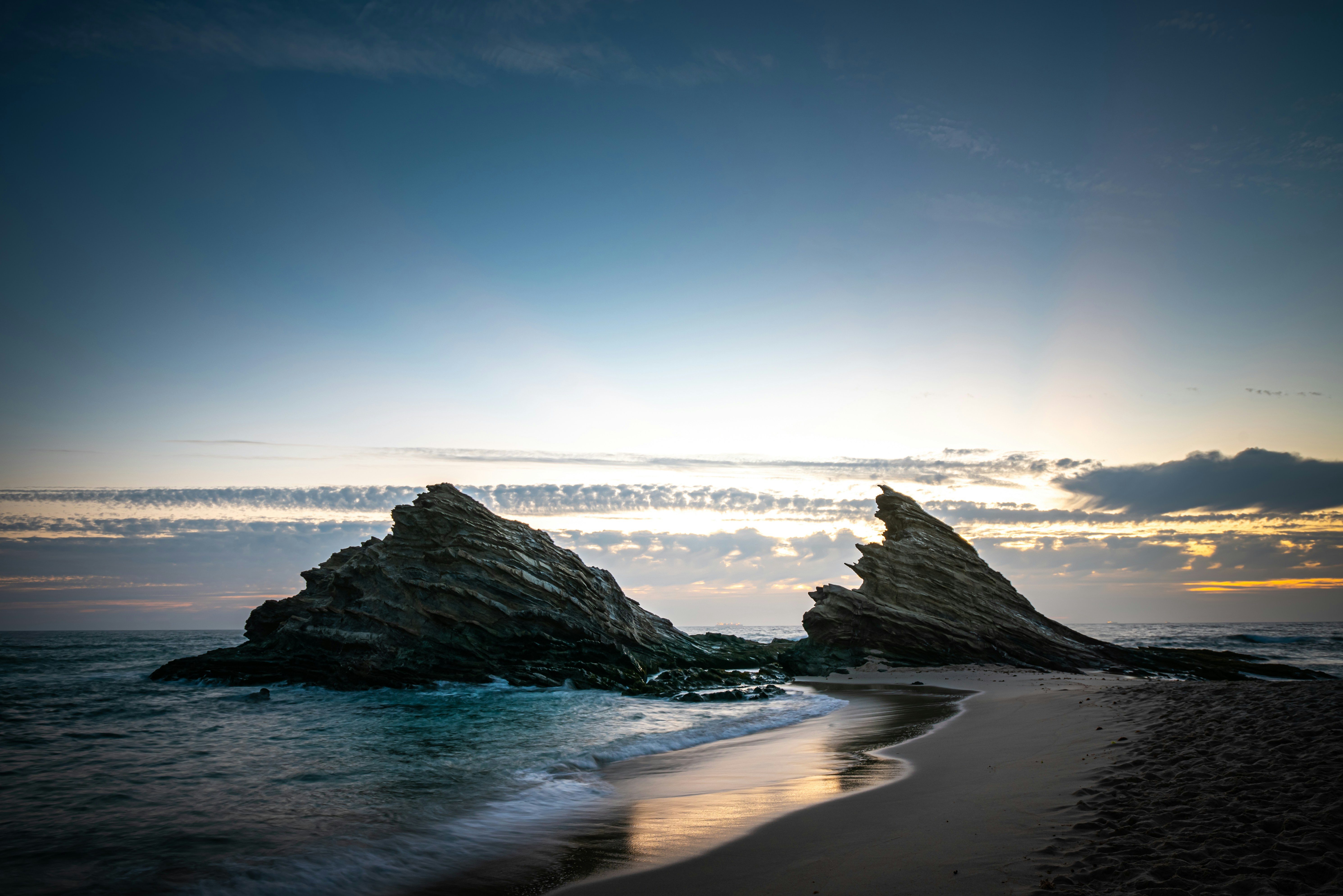Dramatic rock formations meet blurred ocean waves at sunset along the Alentejo coast.