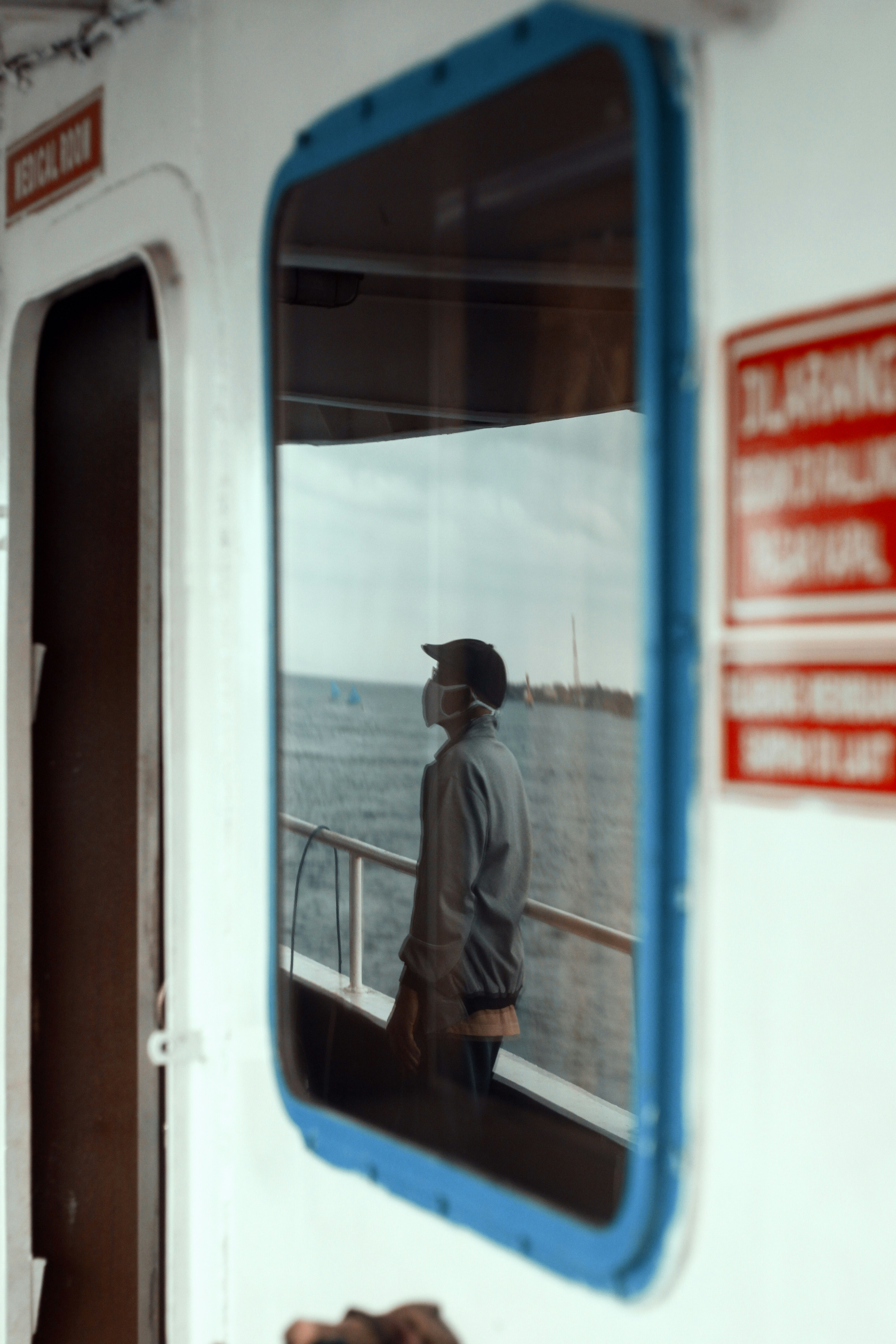 Masked Observer at a Blue-Trim Window: Quiet Vessel Portrait against the Sea