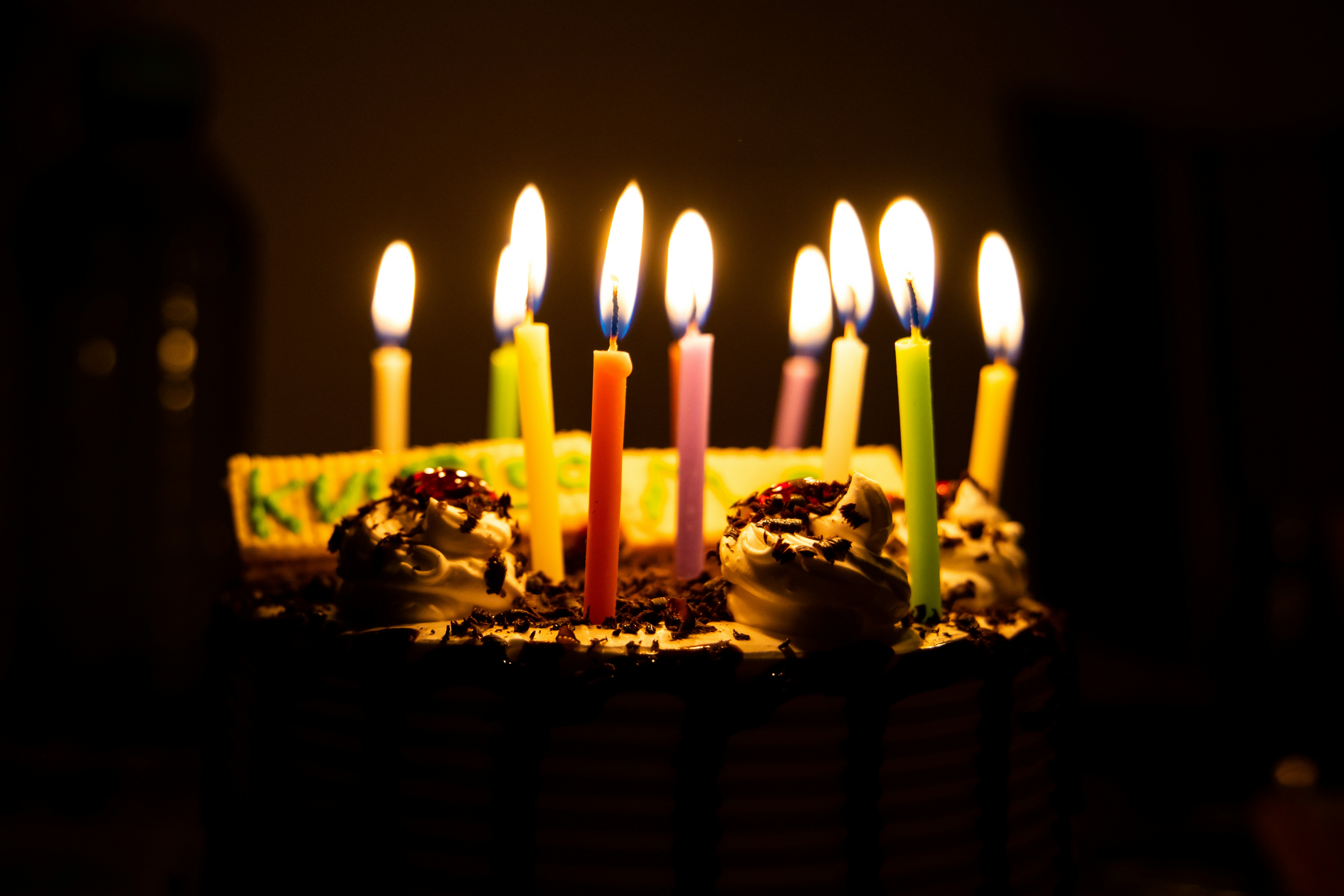 Colorful birthday candles illuminate a decorated cake, creating a warm and festive atmosphere. The scene captures the joy of celebration.