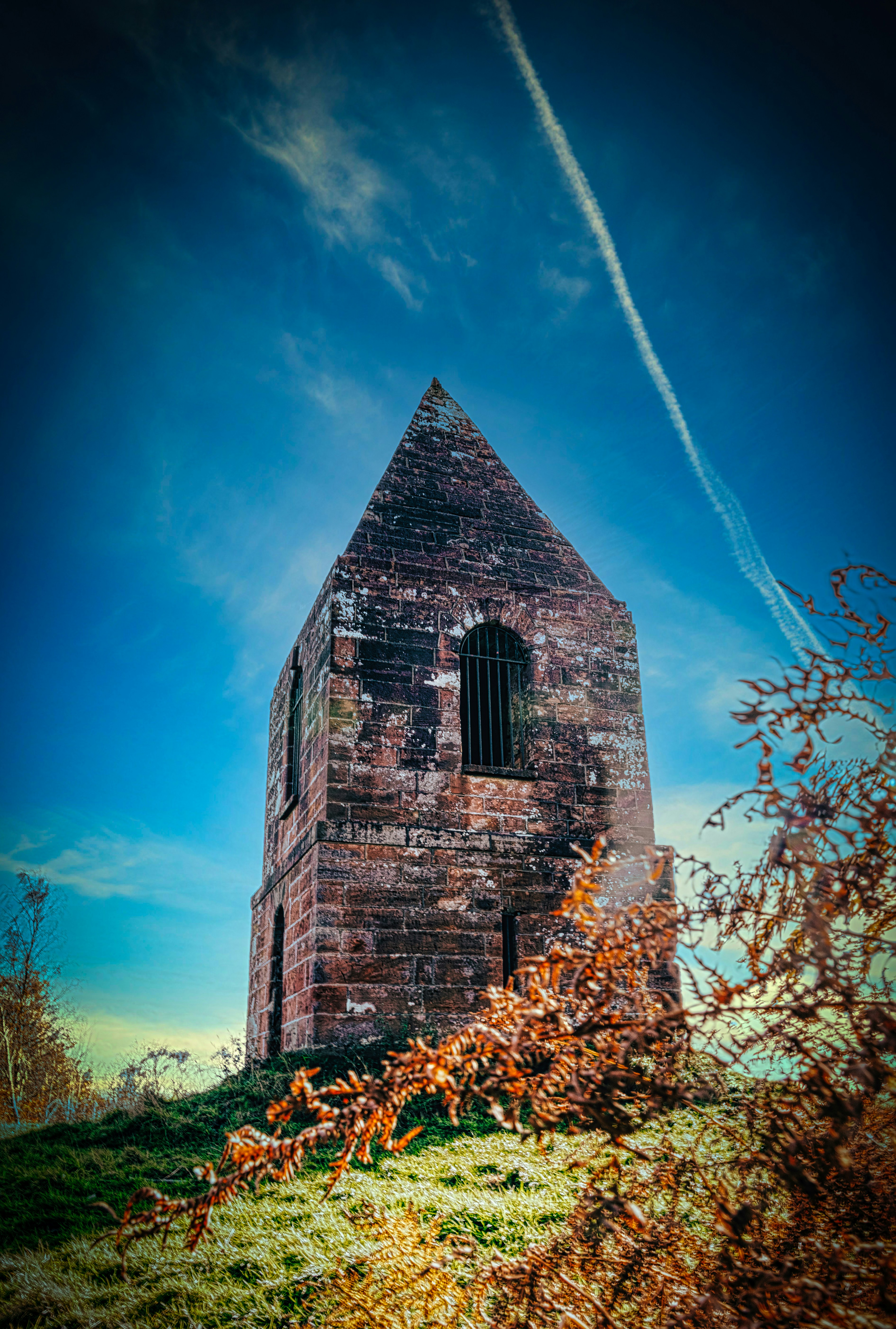 Weathered Brick Spire Against a Cerulean Sky with a Diagonal Contrail