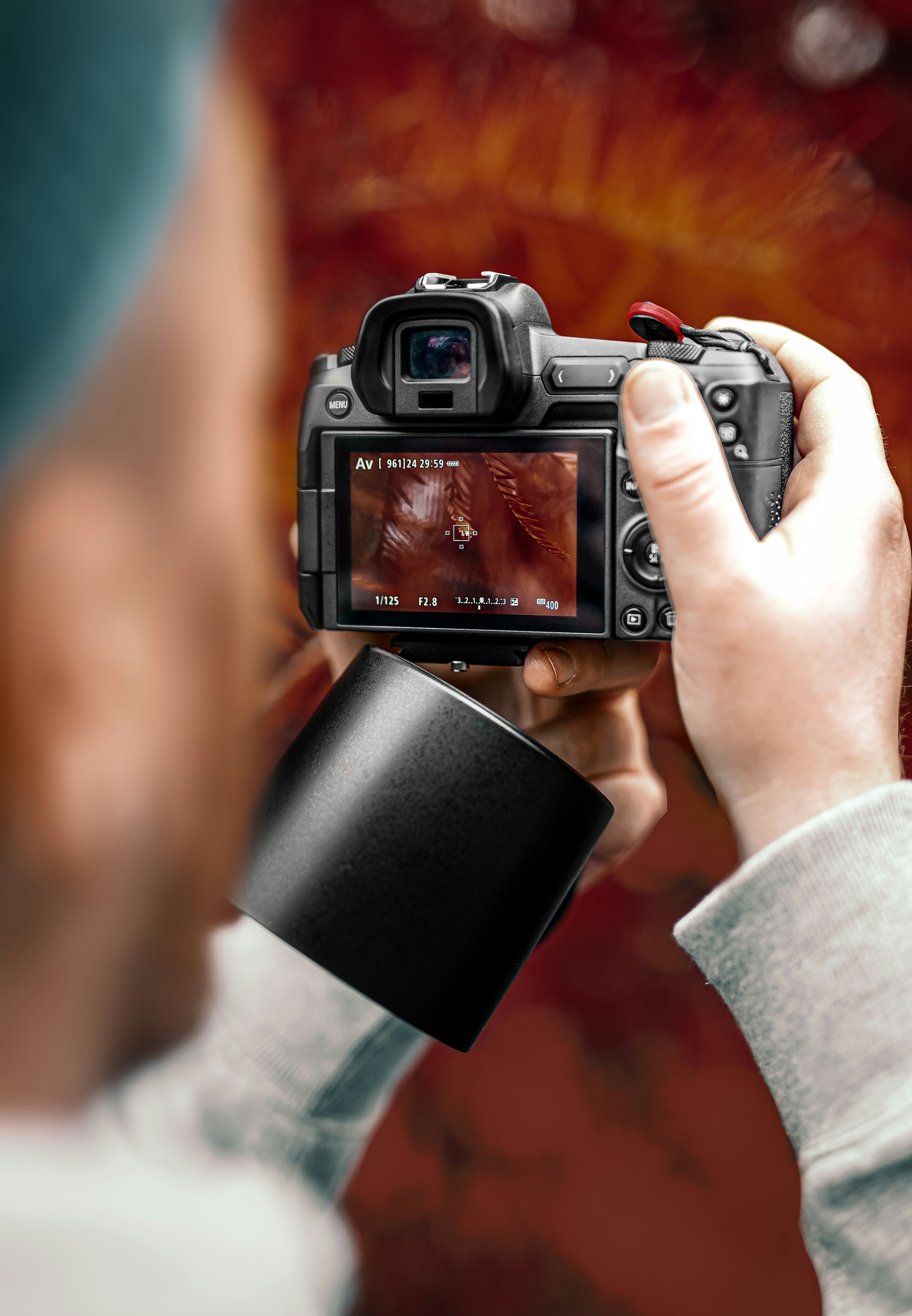 Photographer holding a Canon EOS 5D Mark III, focused on the camera's display showing intricate details of a subject. The background features warm, abstract colors.