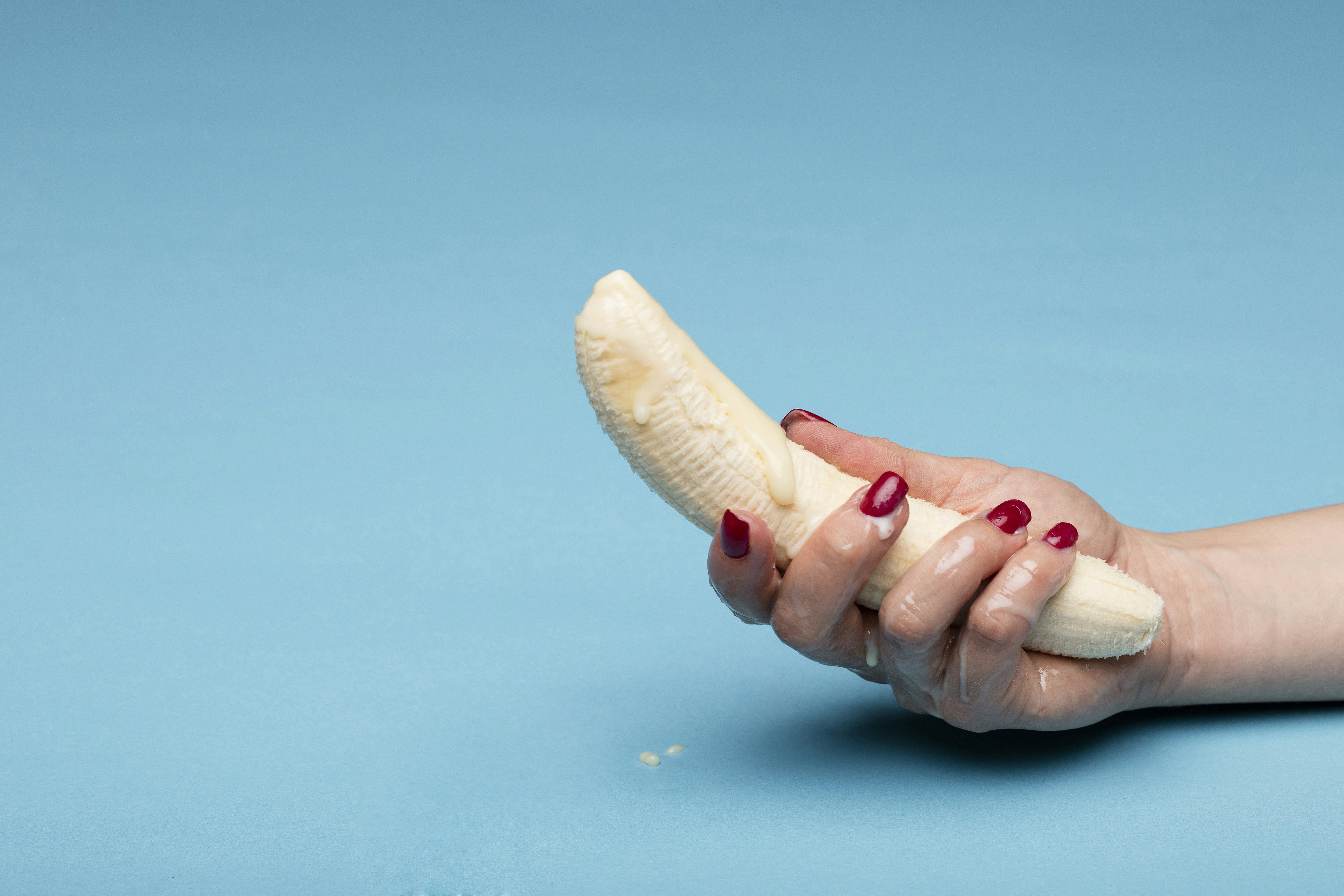 Hand holding a peeled banana against a soft blue background, showcasing a playful contrast in textures and colors.