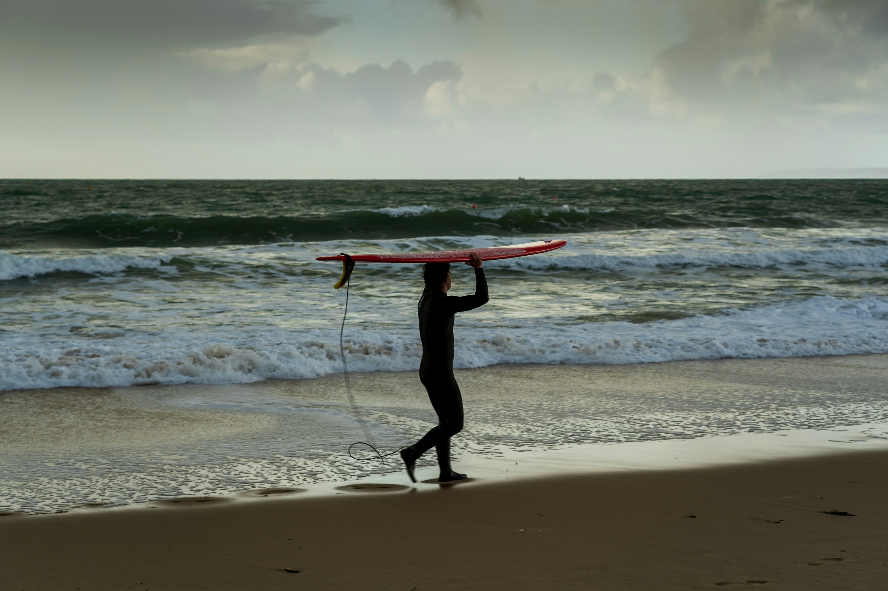Dusk Silhouette: Surfer with a Red Surfboard on a Windy Shore