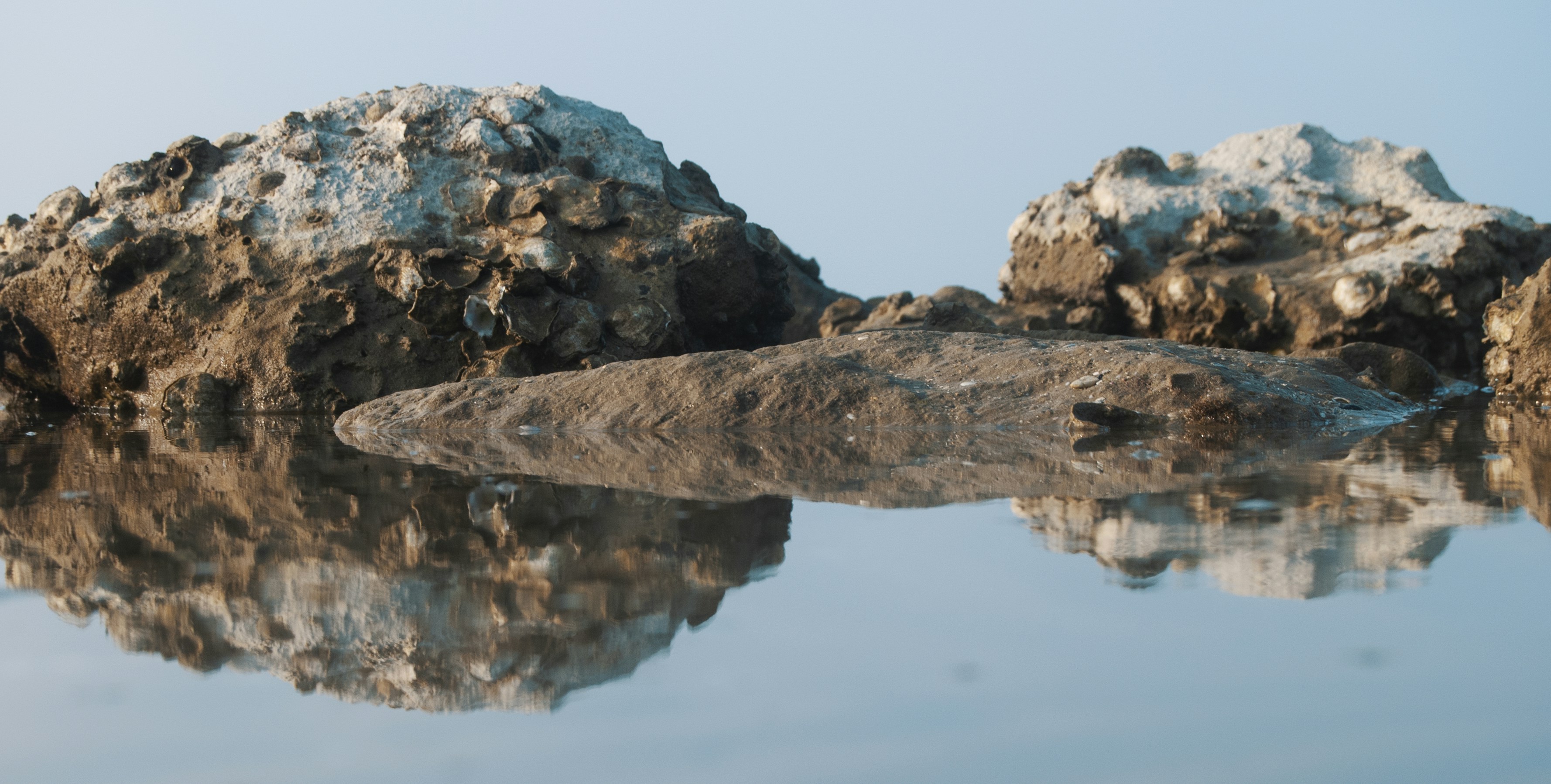 Rocks reflected in calm water under a clear blue sky, creating a symmetrical landscape.