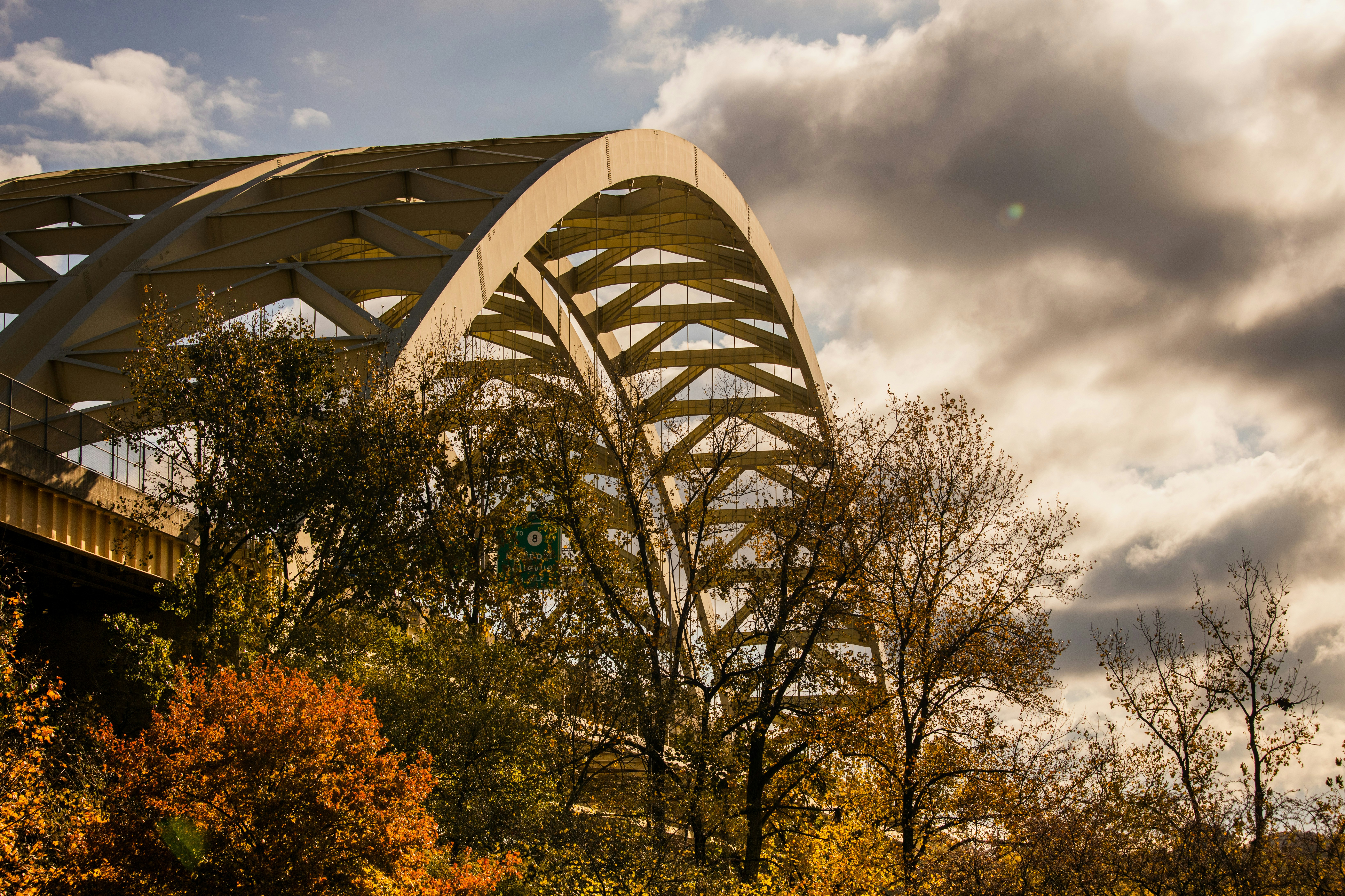 Arched bridge framed by autumn foliage with a backdrop of dramatic clouds.