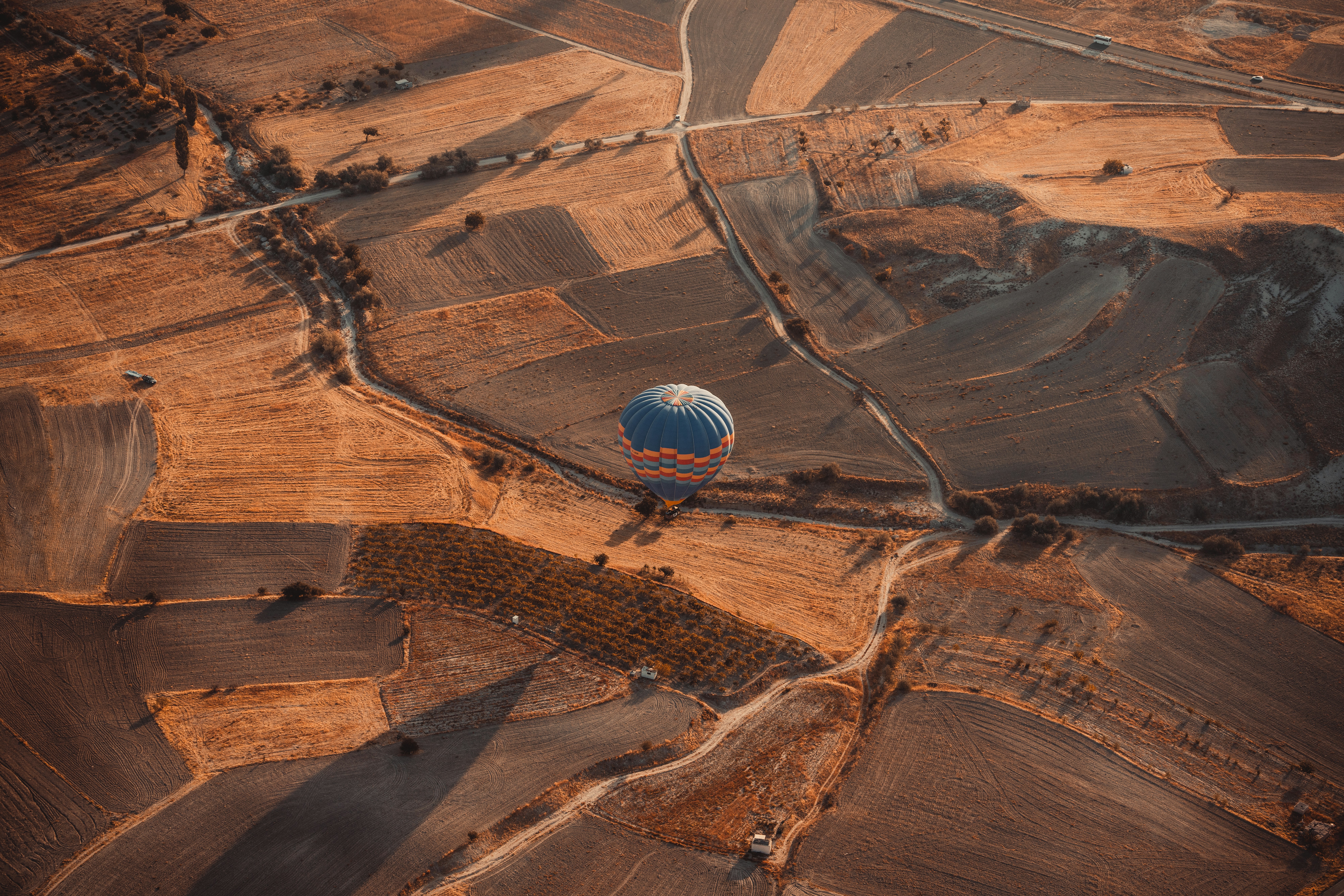 Hot air balloon floating above patchwork fields during golden hour.
