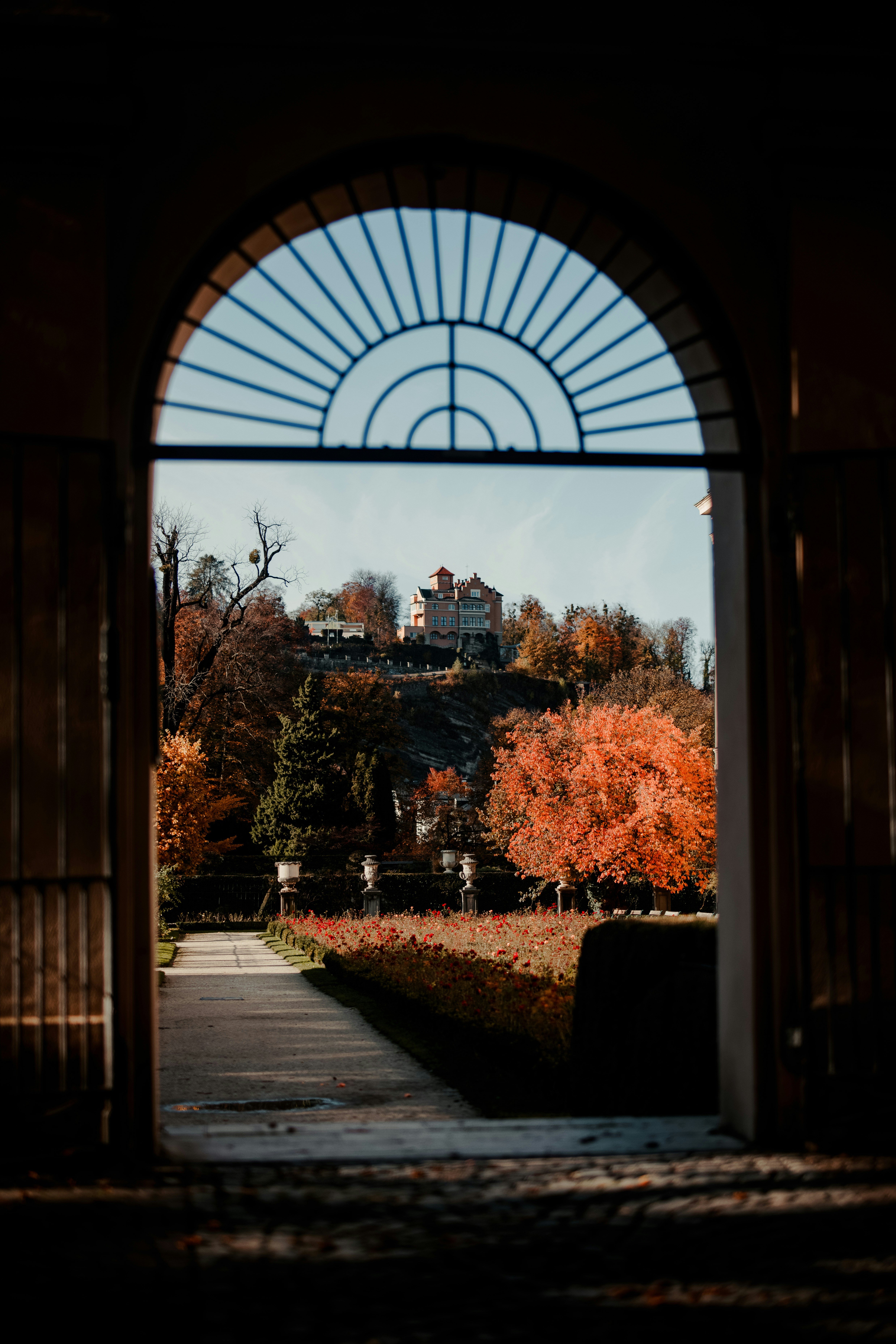 View through an ornate archway showcasing a vibrant autumn landscape with a distant villa atop a hill, surrounded by colorful foliage.