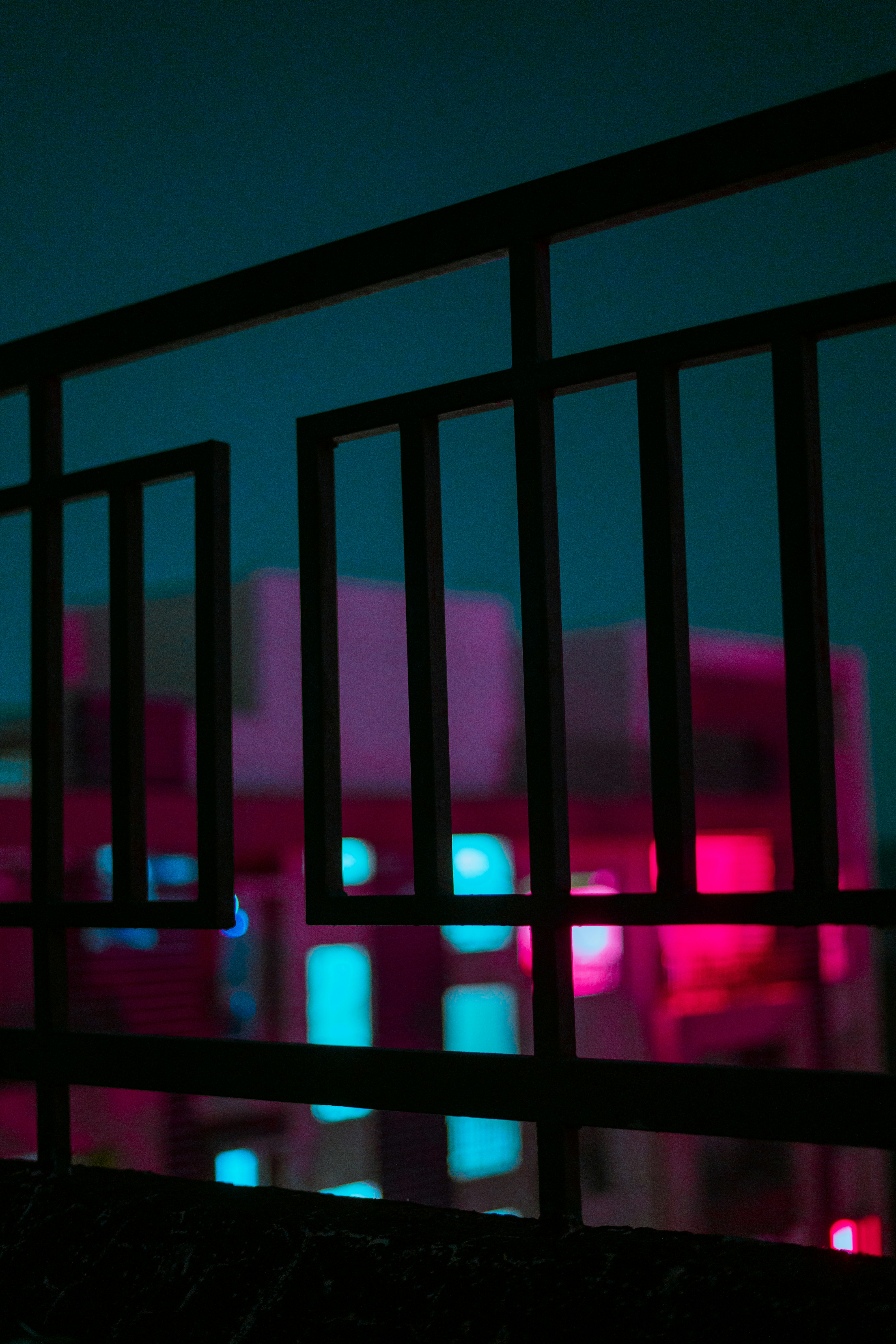 Neon Bokeh Through a City Balcony Railing at Night