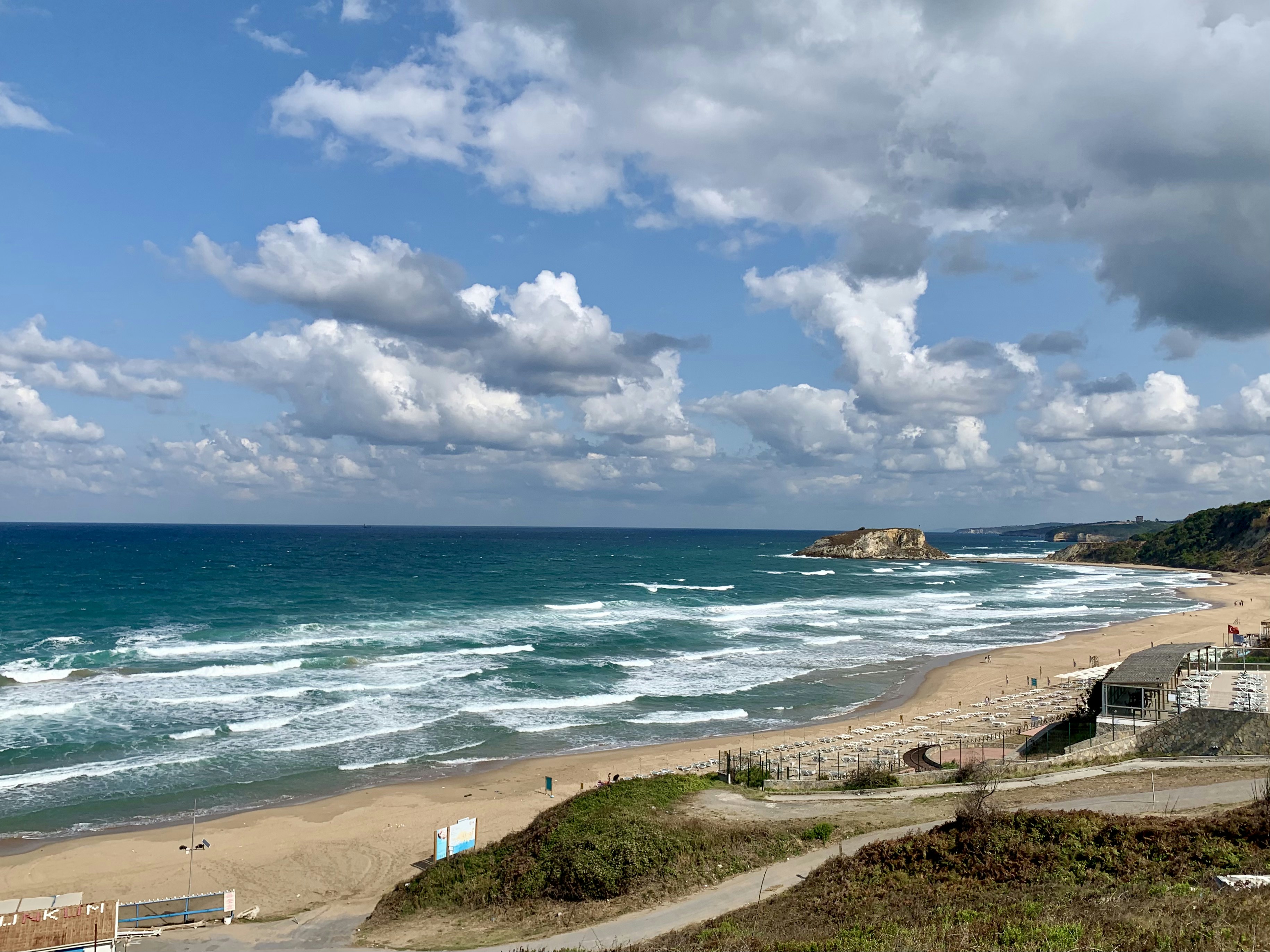 Vibrant waves crash onto a sandy beach under a partly cloudy sky.
