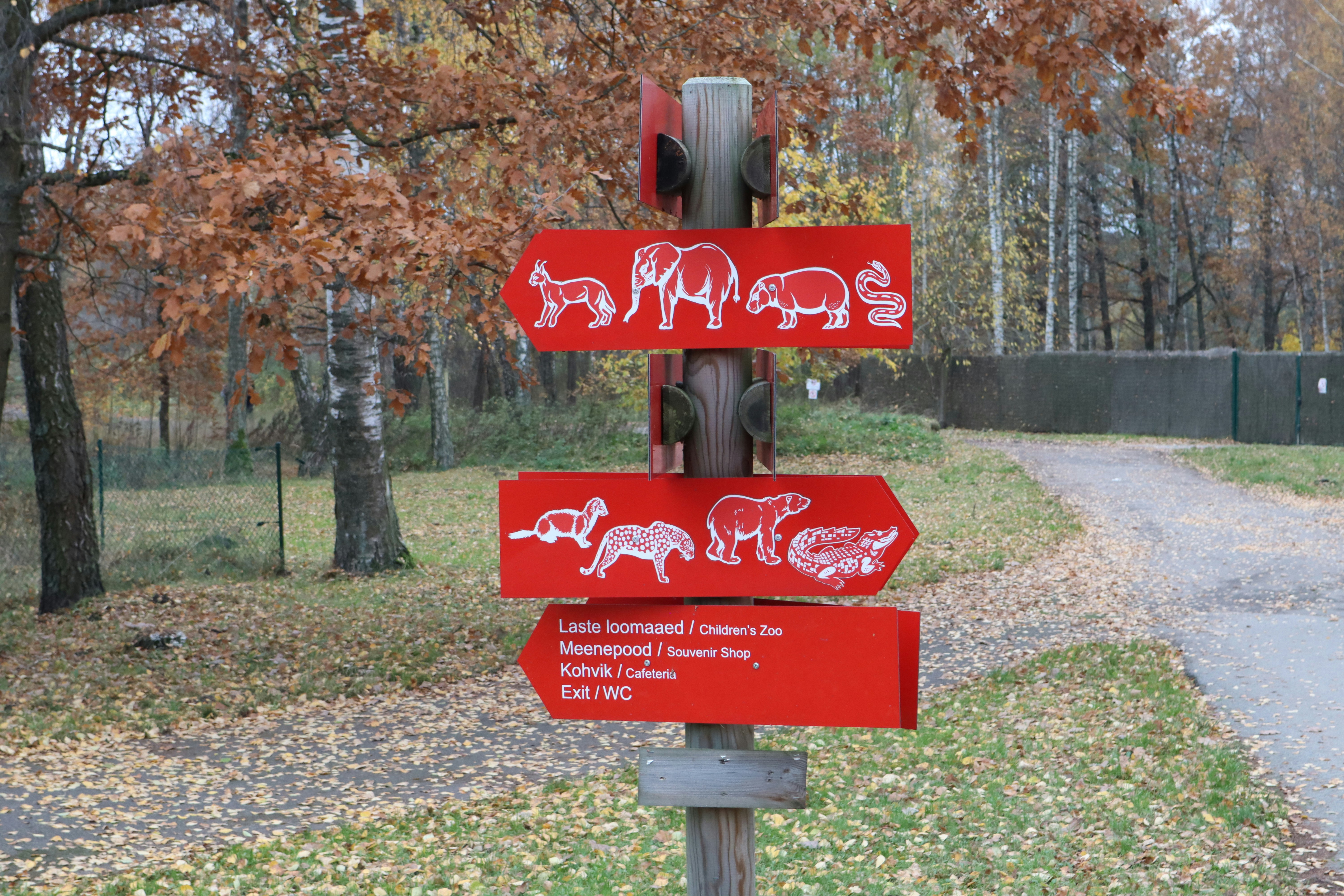Red directional signpost displaying various animal icons, indicating paths to different attractions in a zoo setting.