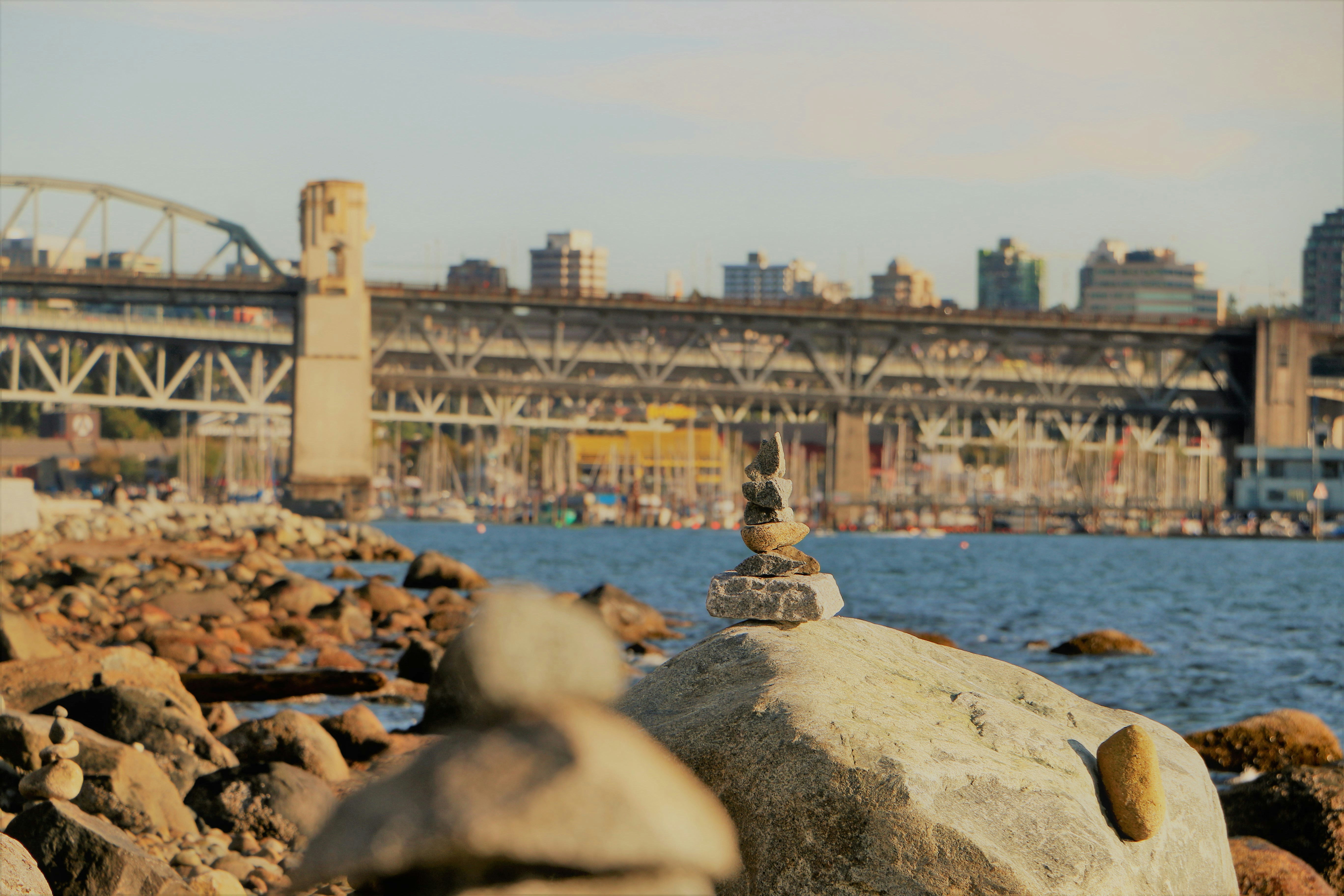 Stacked cairns at the water’s edge with a distant bridge