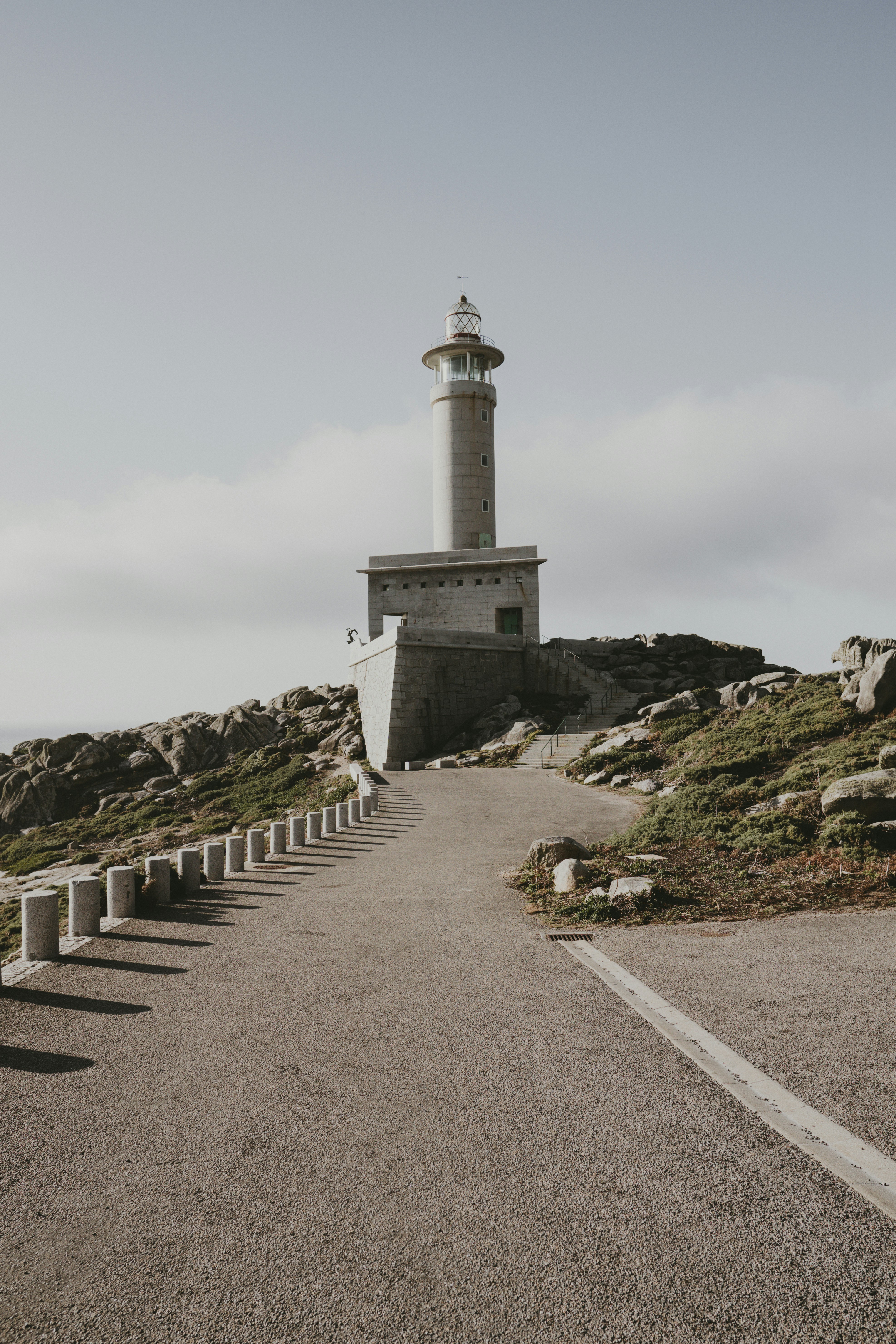 White concrete lighthouse on gray rocky hill under gray sky during ...