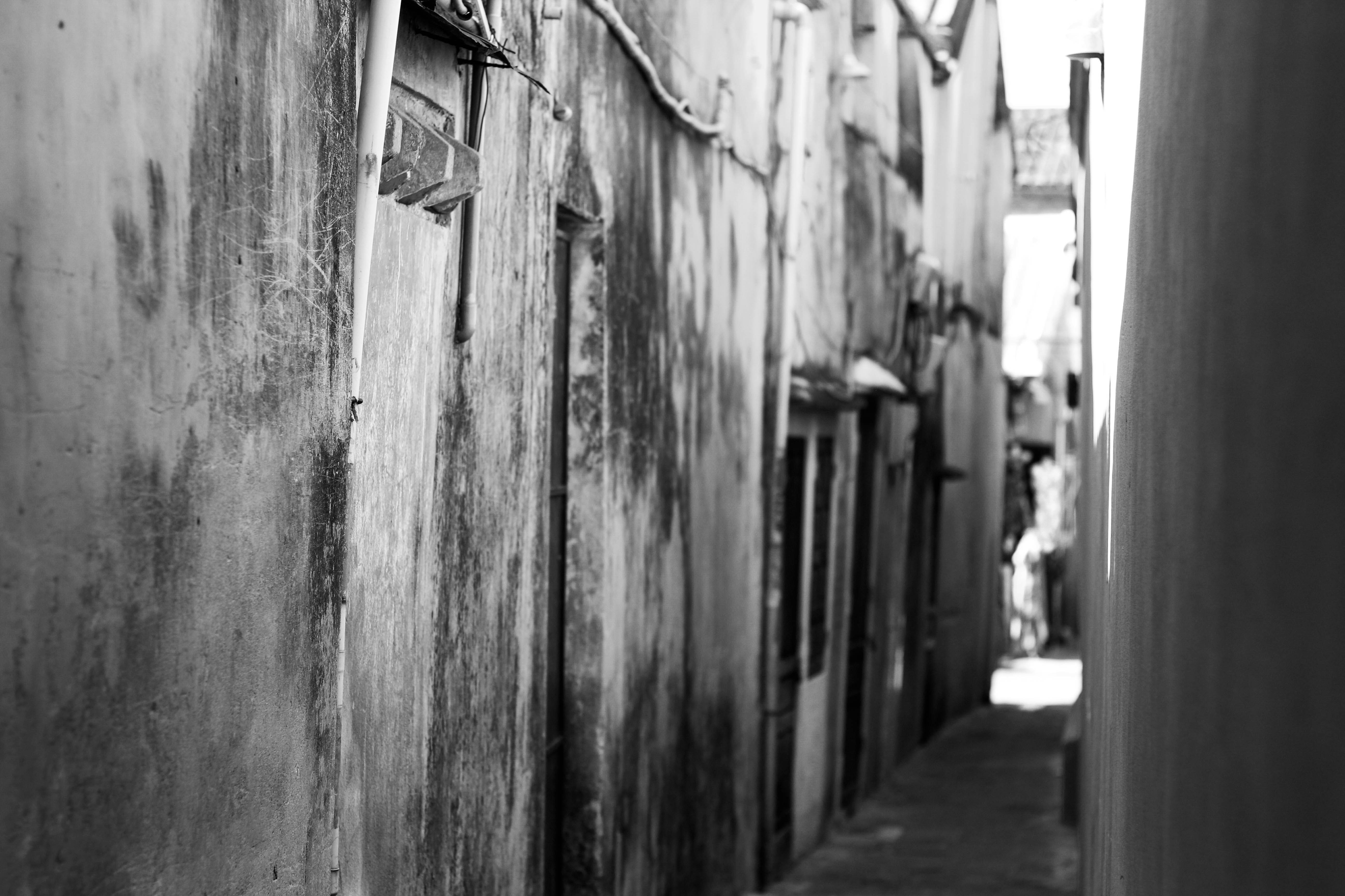 Narrow alleyway lined with weathered walls in black and white.