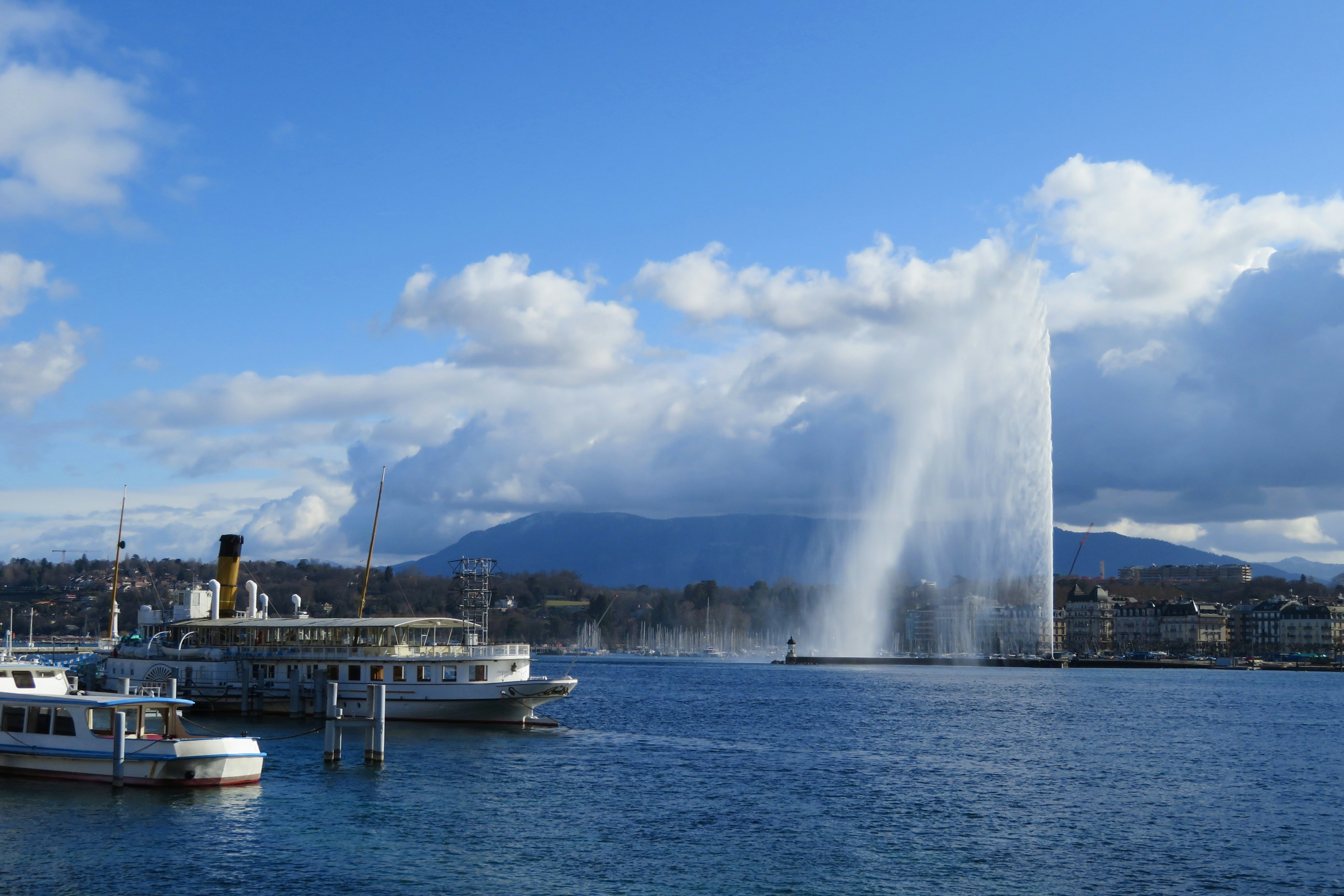 White and blue ship on a calm sea with a dramatic water fountain spraying under a vibrant blue sky.
