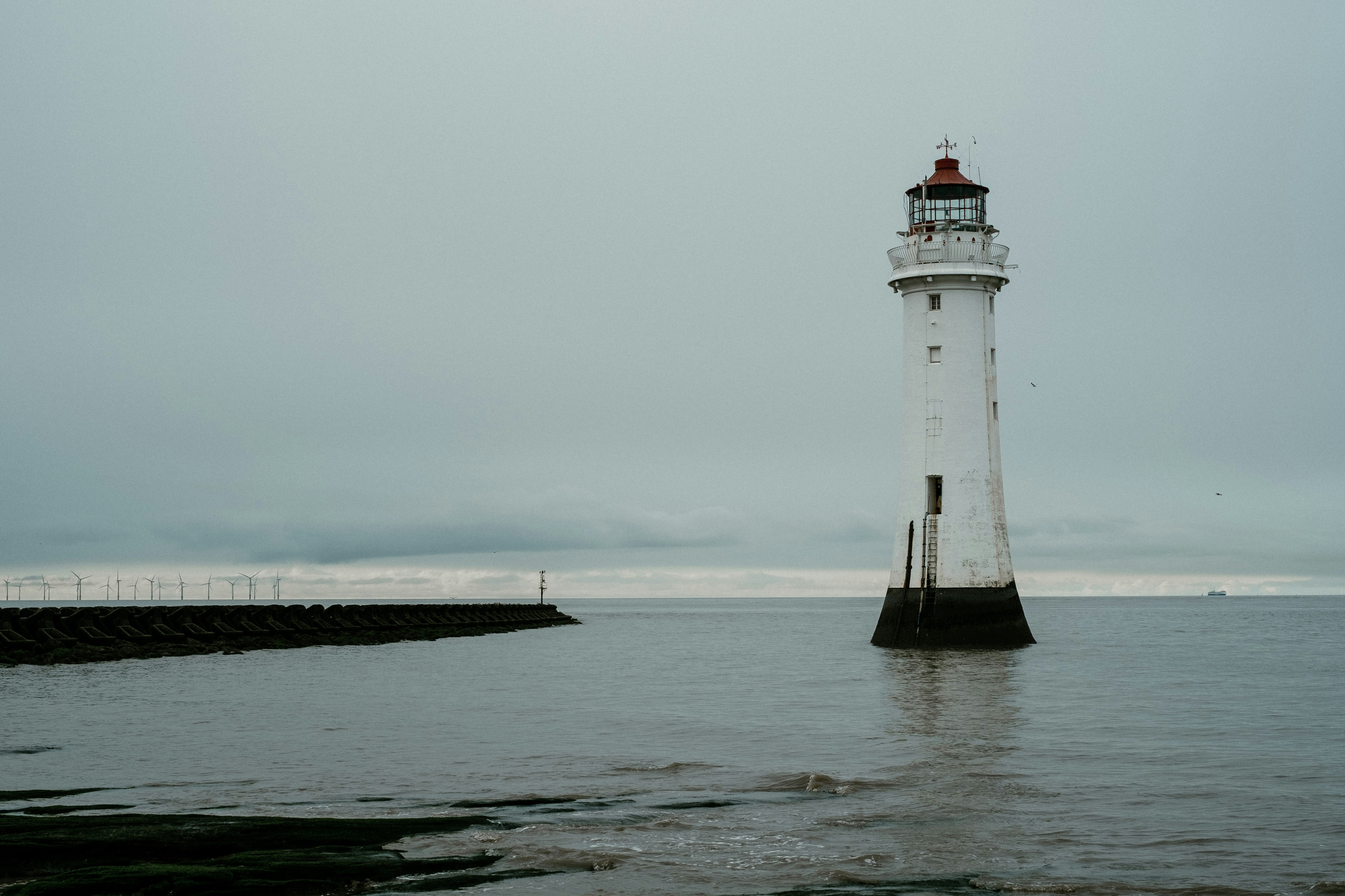 White and black lighthouse standing on a sea dock under a cloudy sky during daytime.